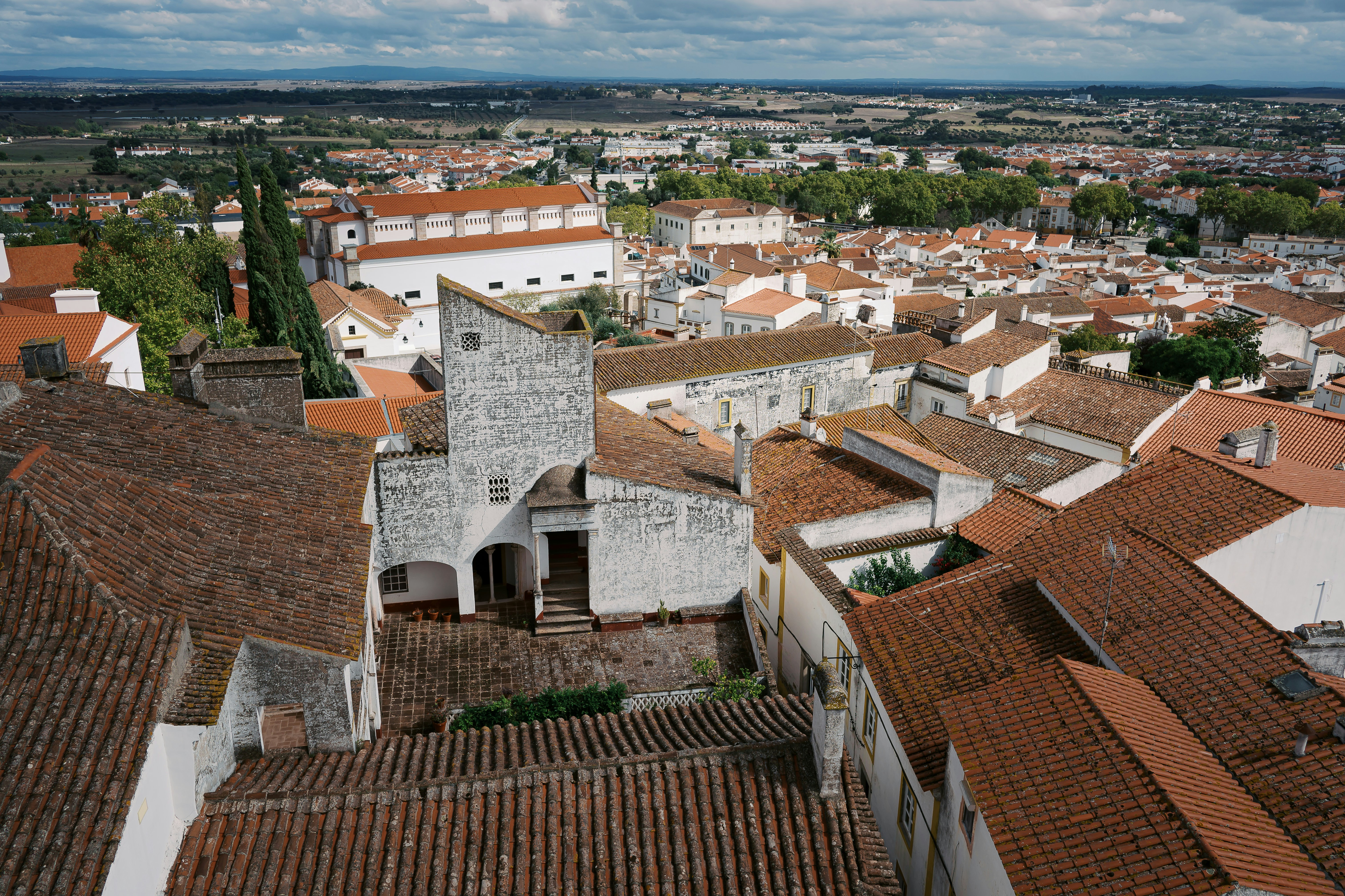 Panoramic view over Évora's terracotta rooftops from the cathedral, with distant landscapes under a cloudy sky.