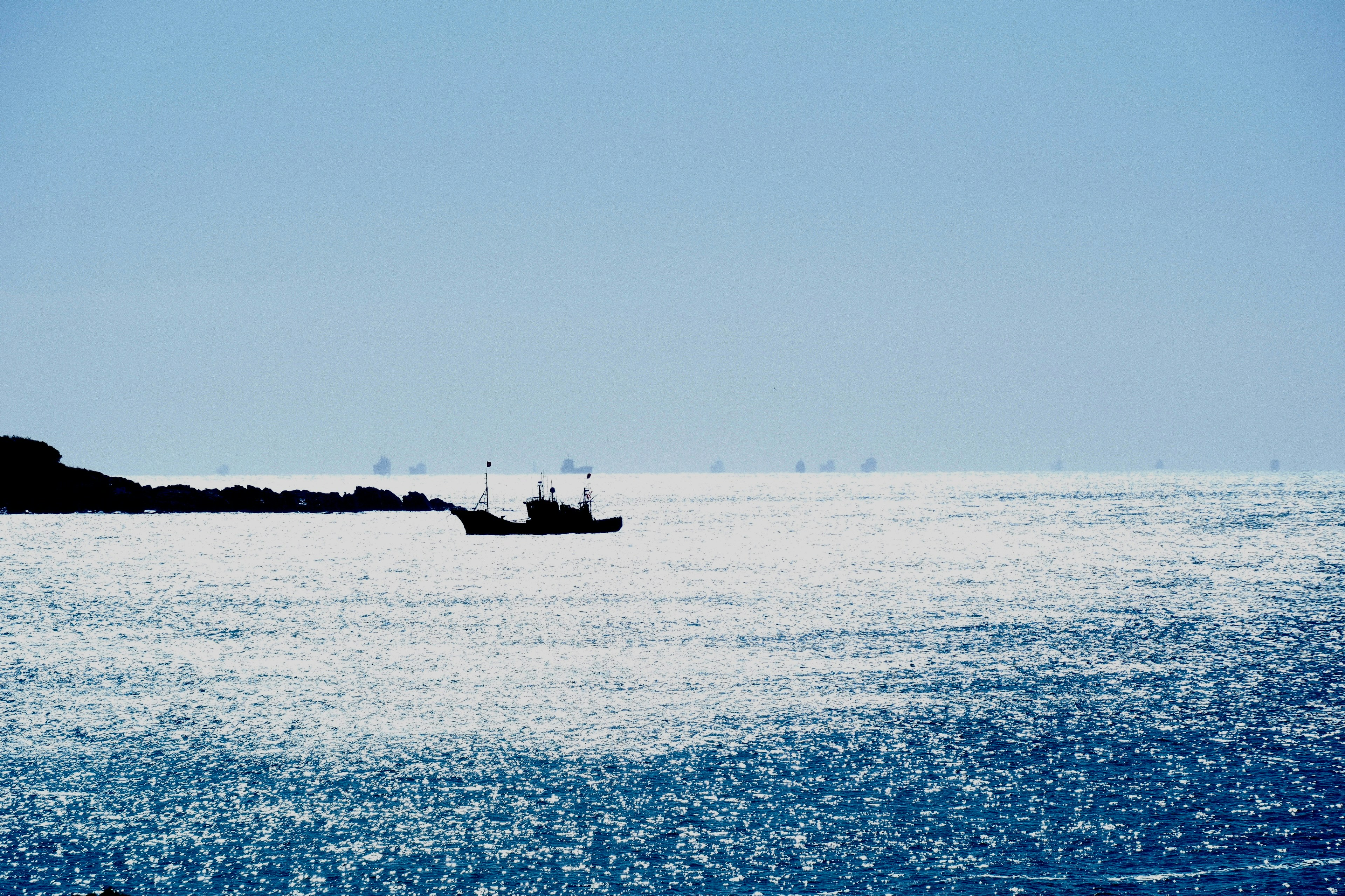 Fishing boat silhouetted against a sparkling sea under a clear blue sky.