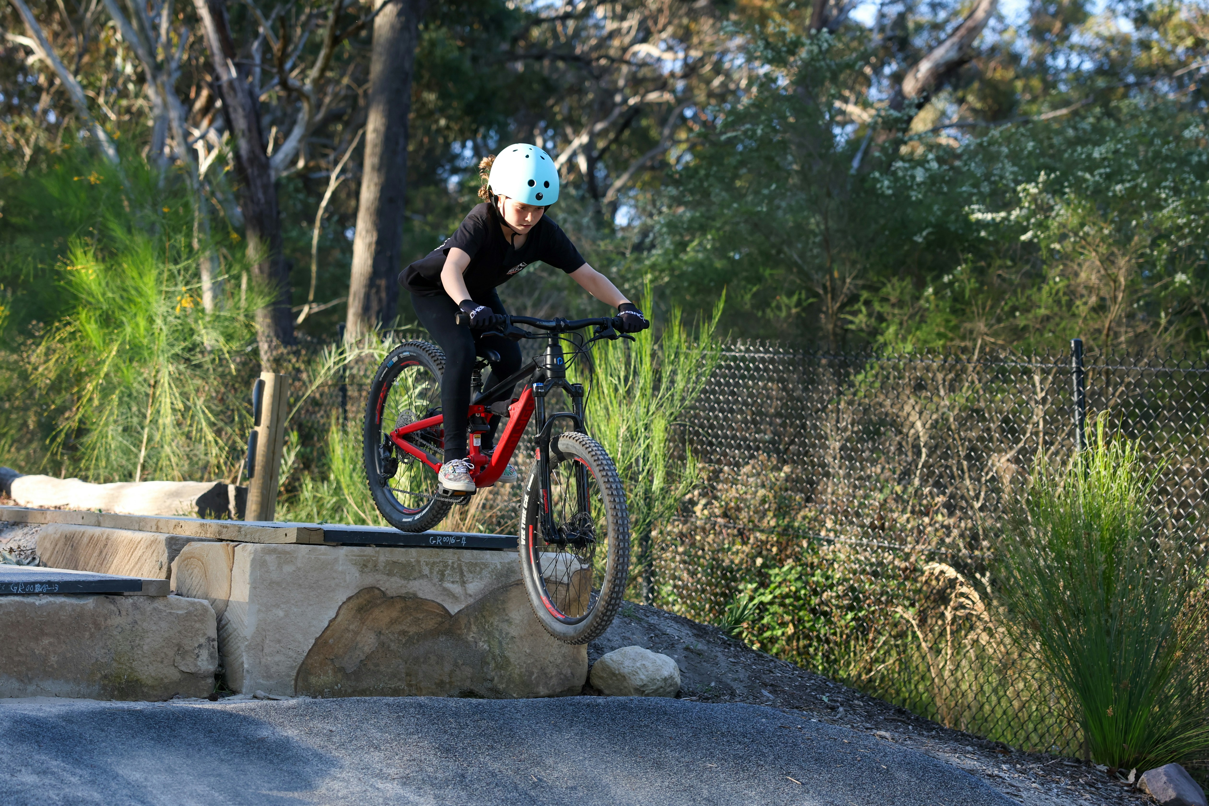 A girl riding a mountain bike off a drop.