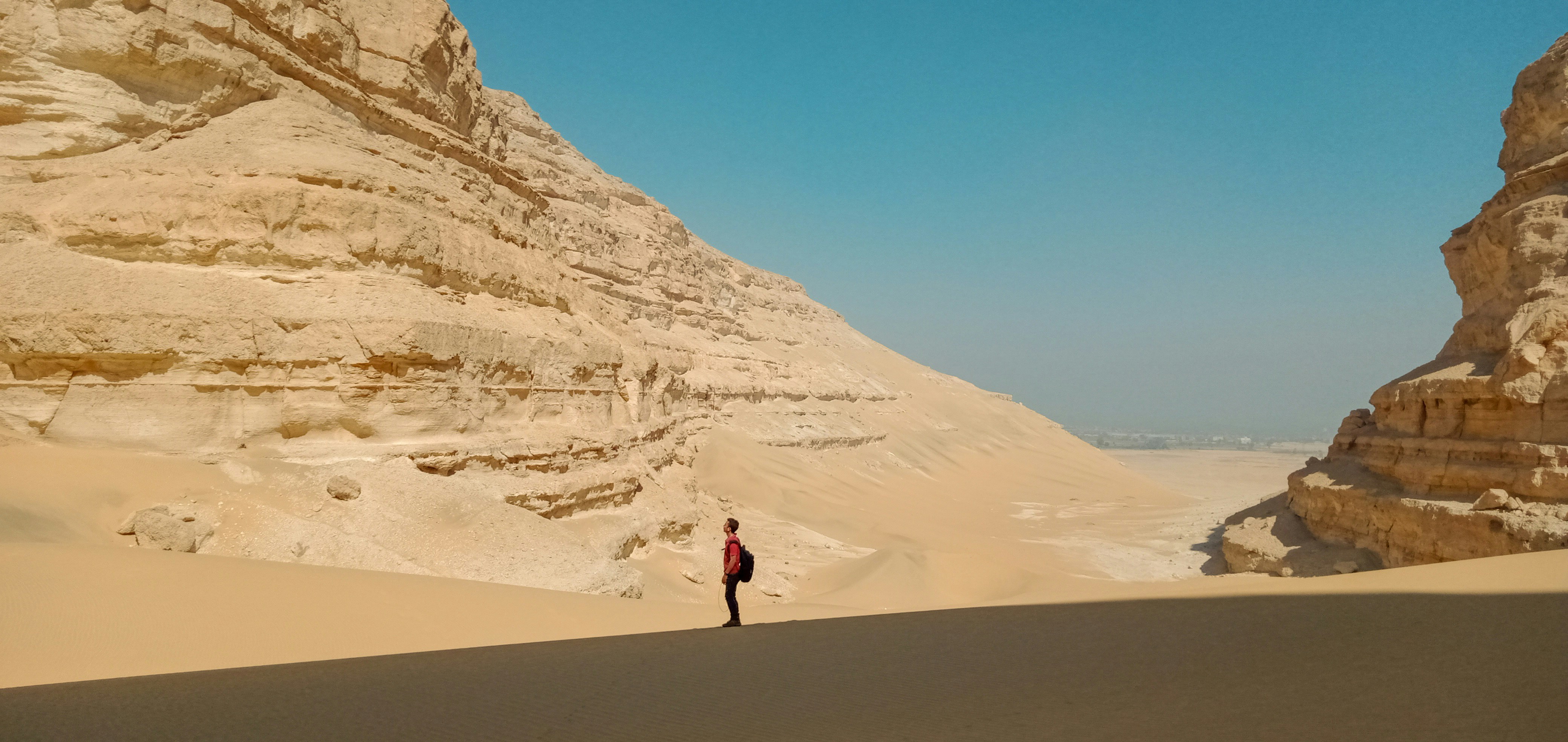 Lone figure standing amidst towering desert dunes under a clear blue sky.