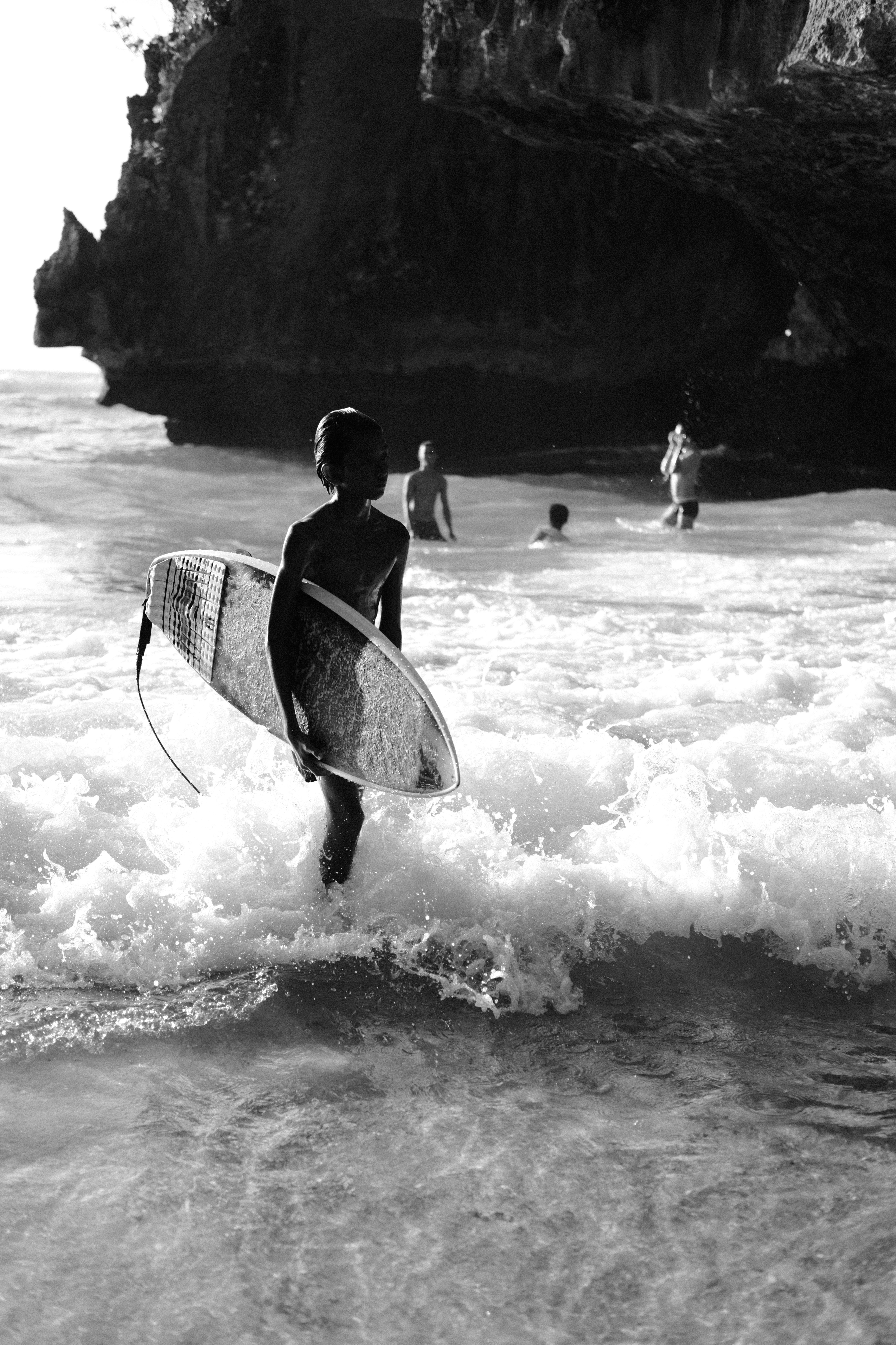 Silhouette in the Surf: A lone surfer strides through whitecaps beside a shadowed cliff