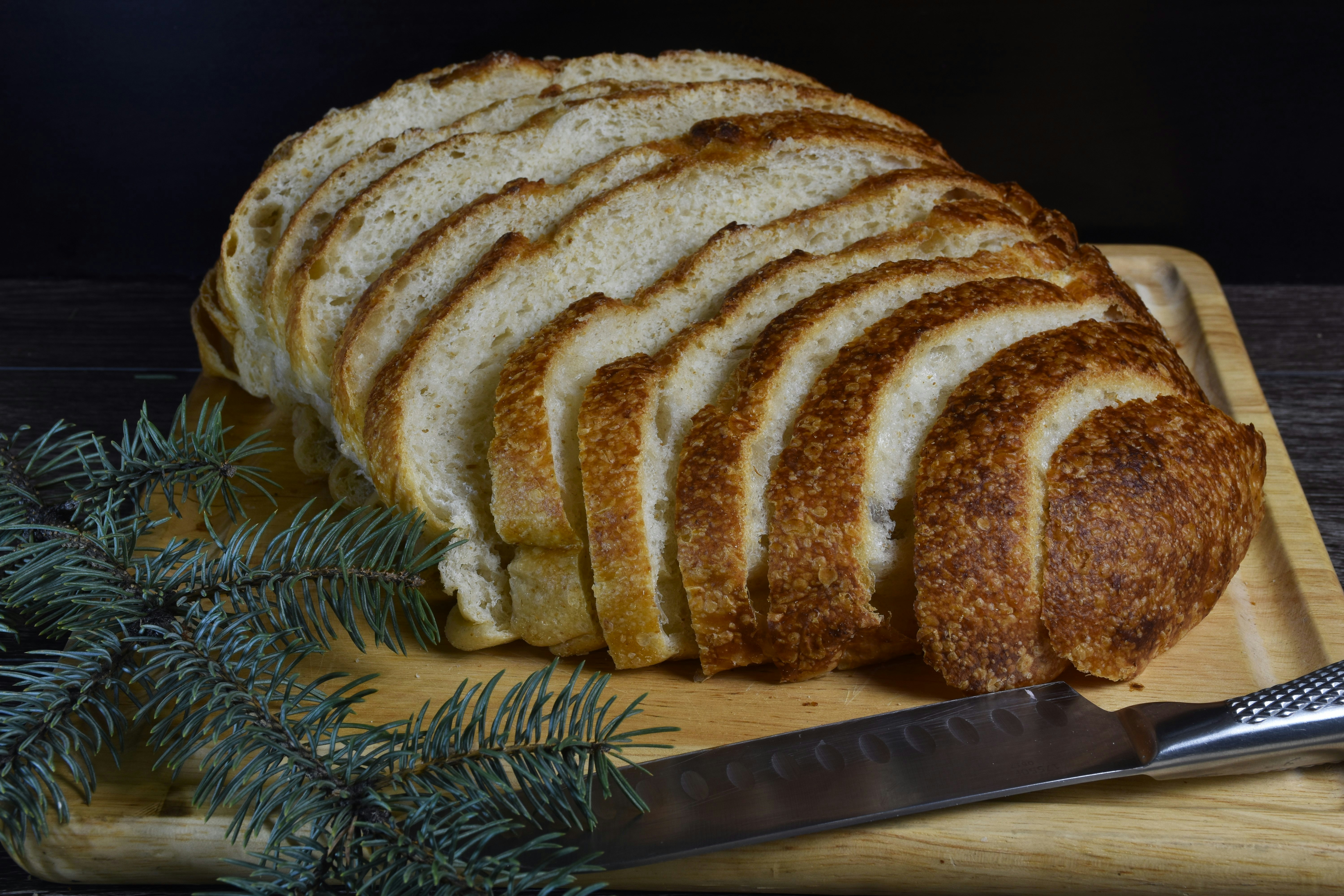 Rows of Sliced Brioche on a Wooden Board with Sprigs and Knife