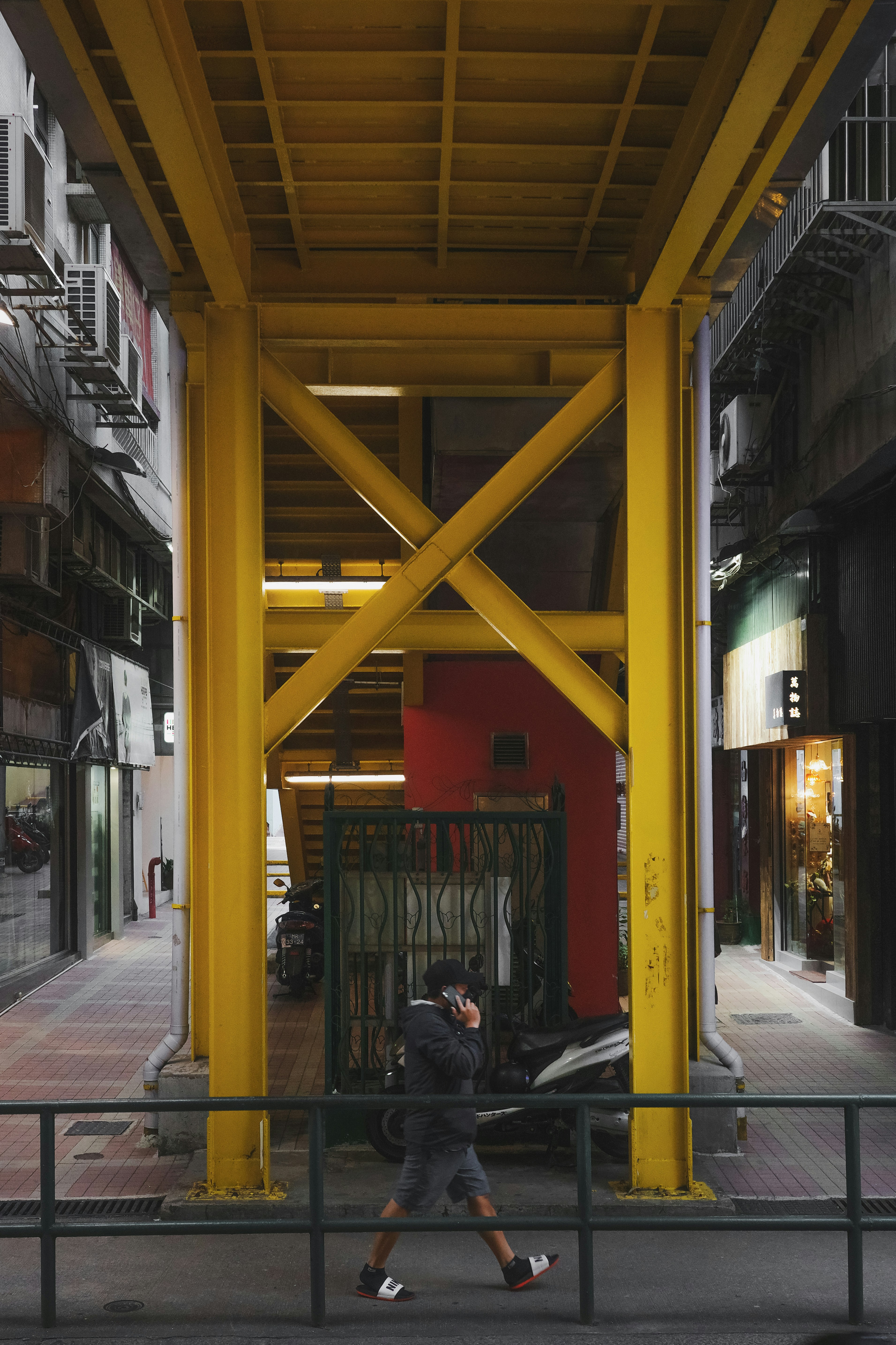 Golden X Under City Canopy: A lone pedestrian framed by yellow steel under an urban overpass