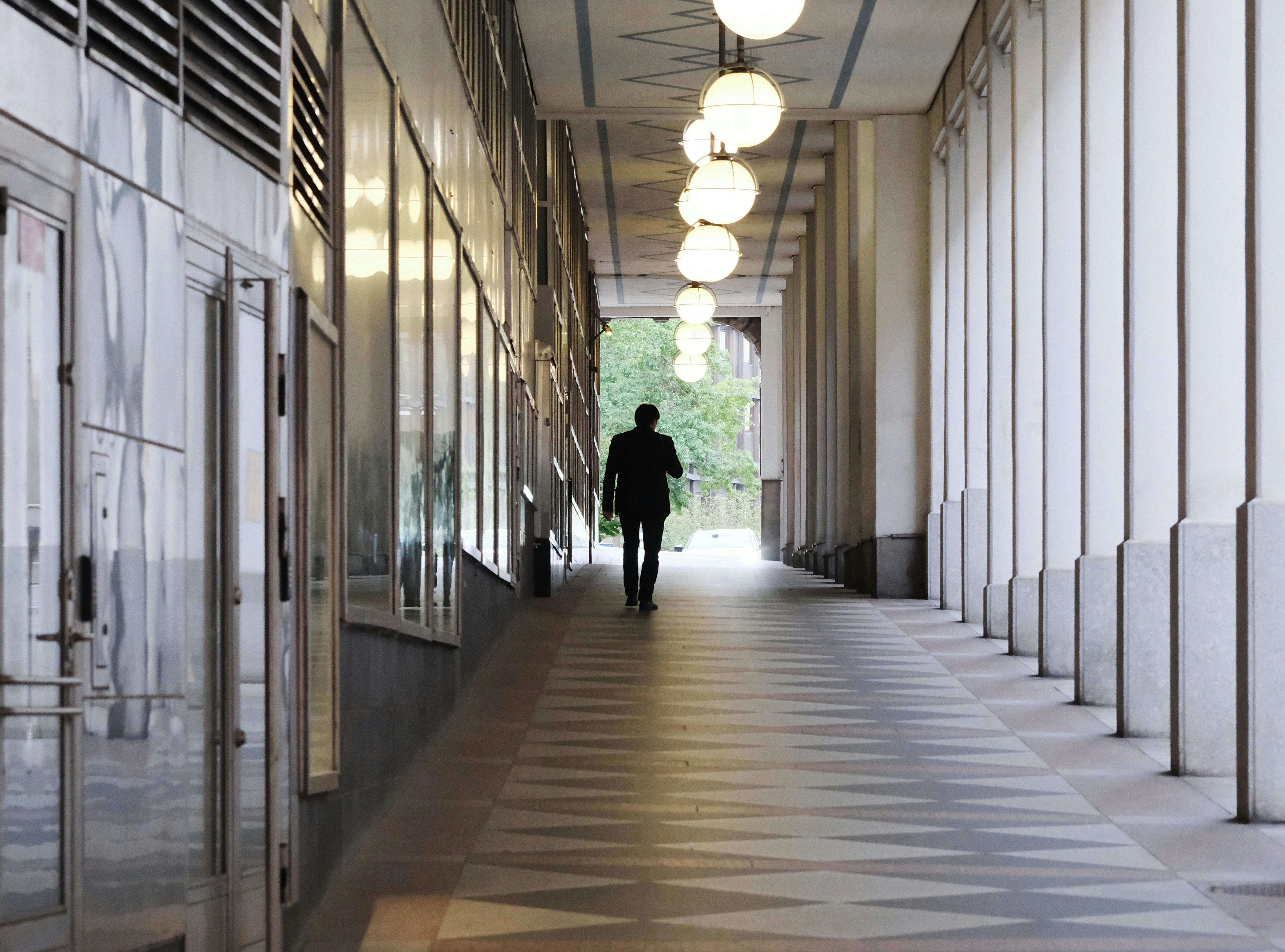 Silhouette of a lone figure walking down a corridor illuminated by pendant lights, showcasing a blend of modern design and serene atmosphere.
