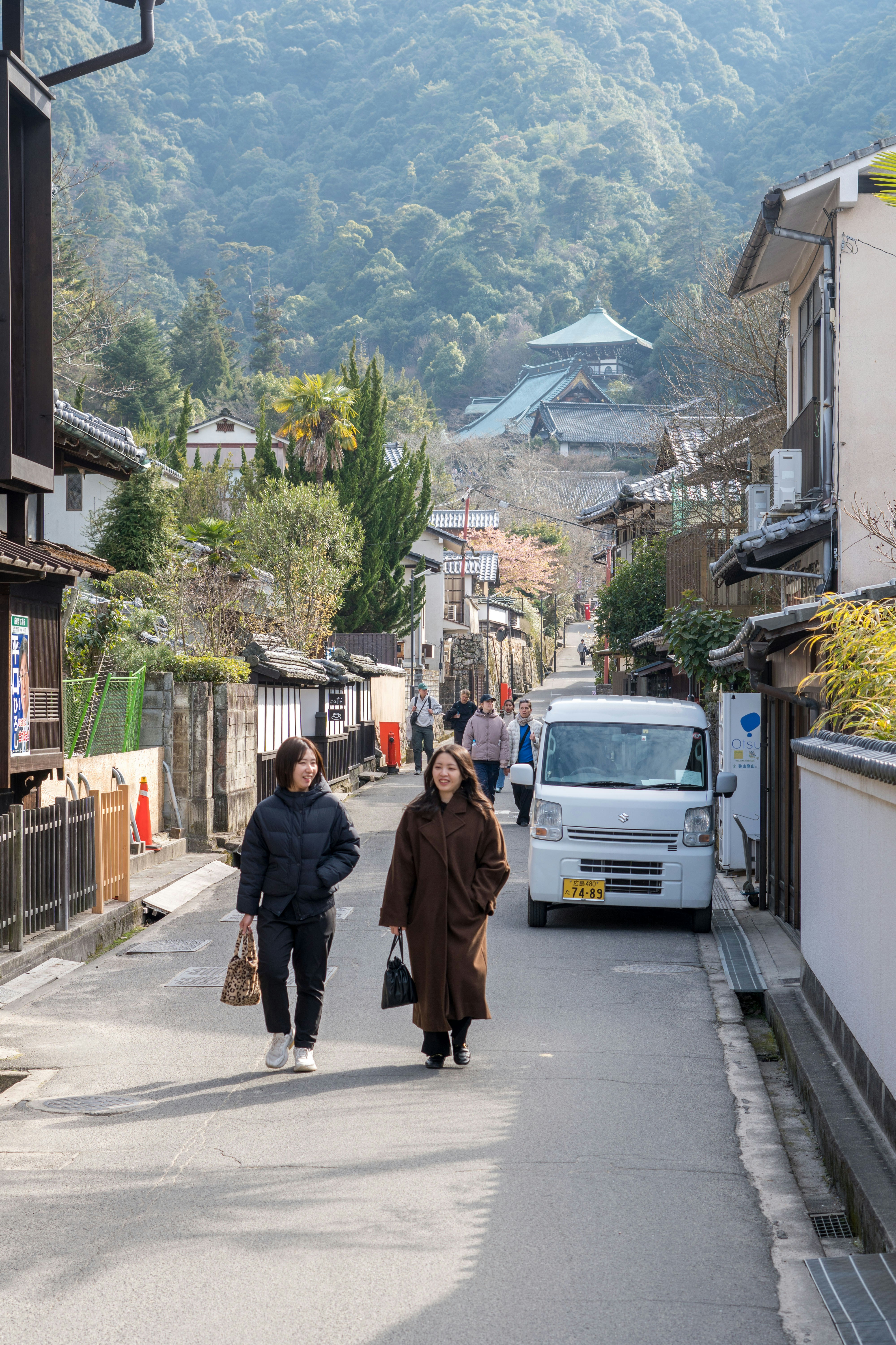 Sunlit Street in a Mountain Village: Two Women Walk Past Traditional Japanese Homes