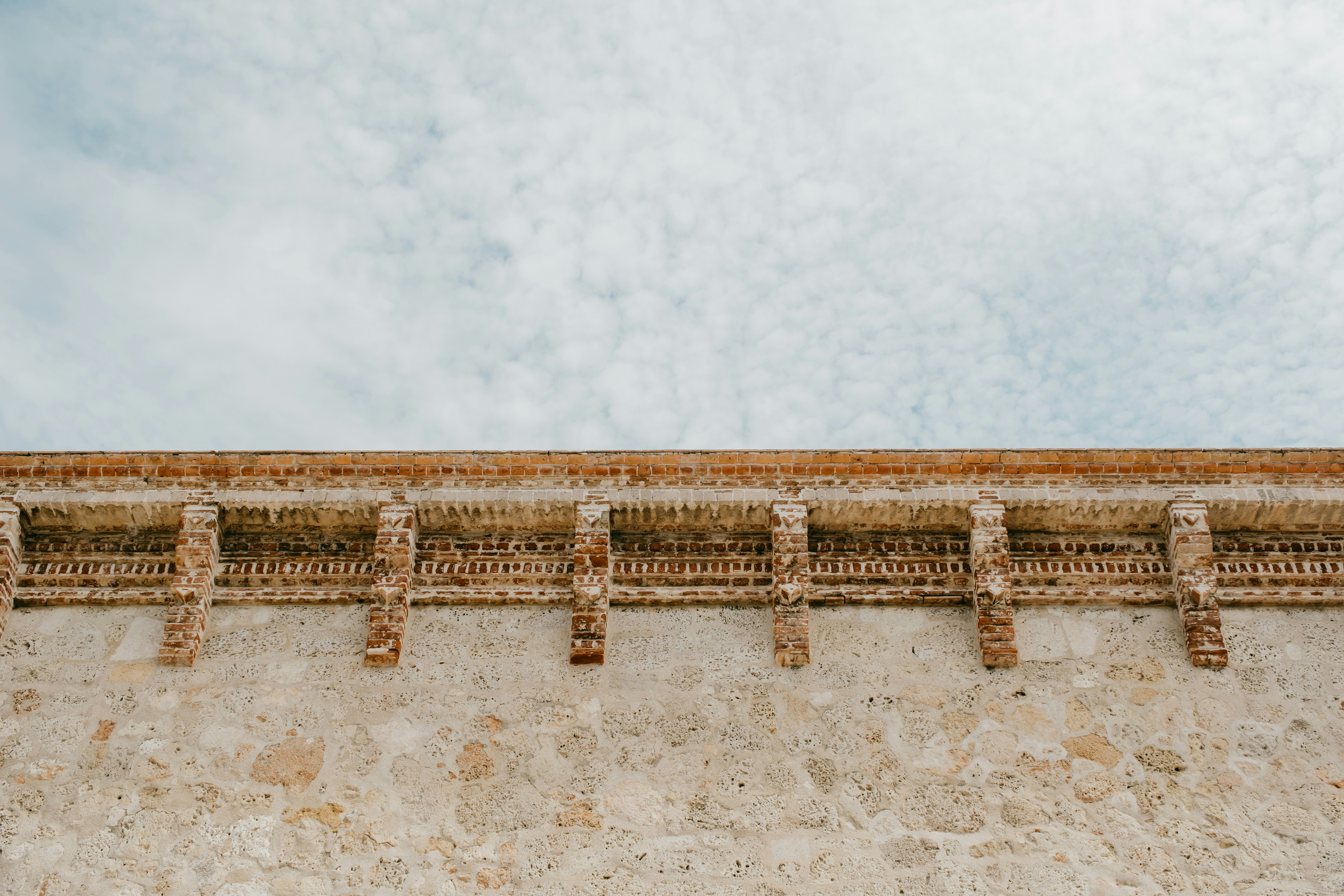 Ancient stone wall adorned with intricate brickwork under a textured sky, showcasing architectural elegance.
