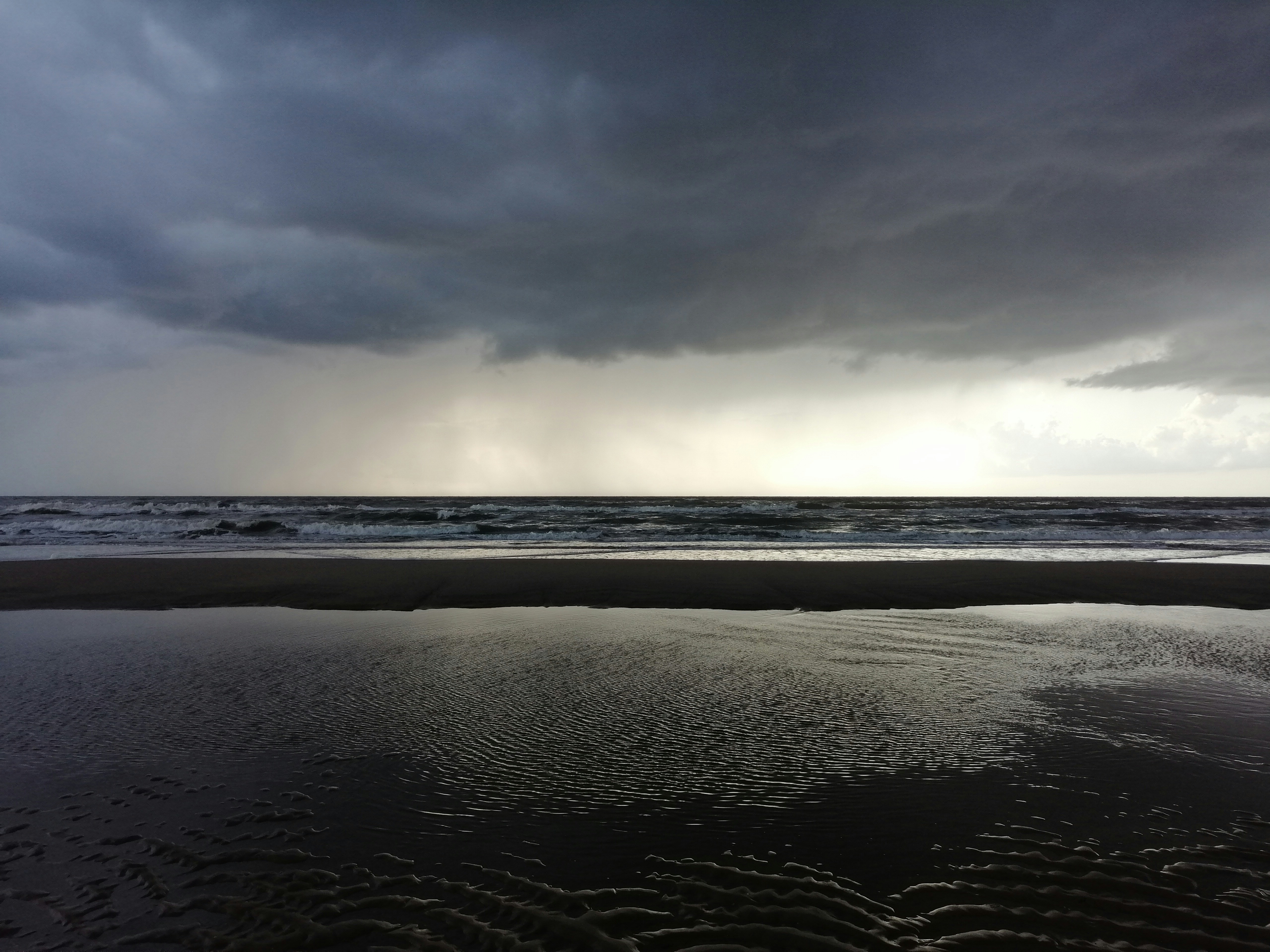 Stormy coast with dark clouds over the horizon and tidal pools reflecting muted light; a moody coastline photograph.