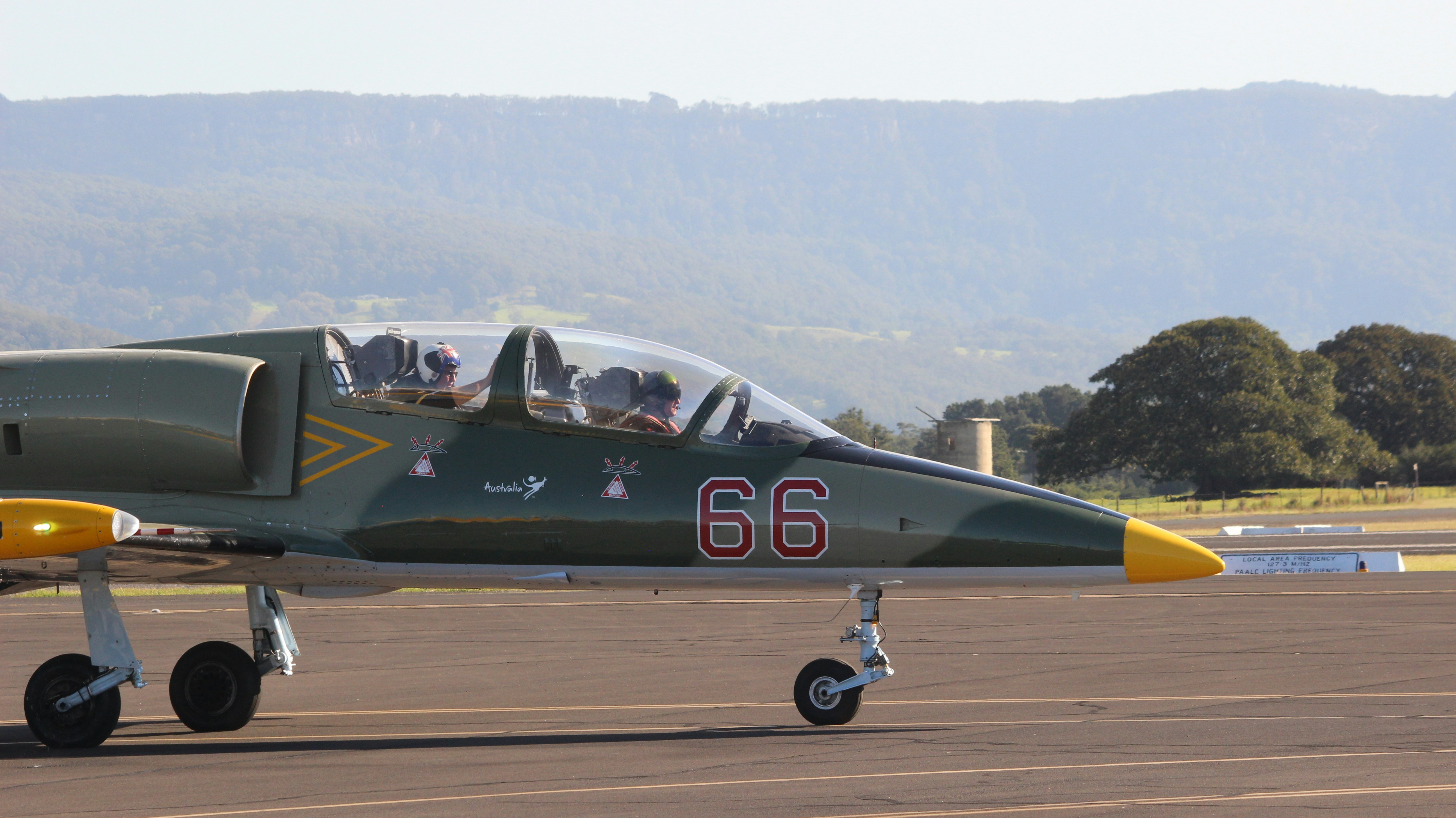 Green tandem-cockpit trainer on a sunlit runway