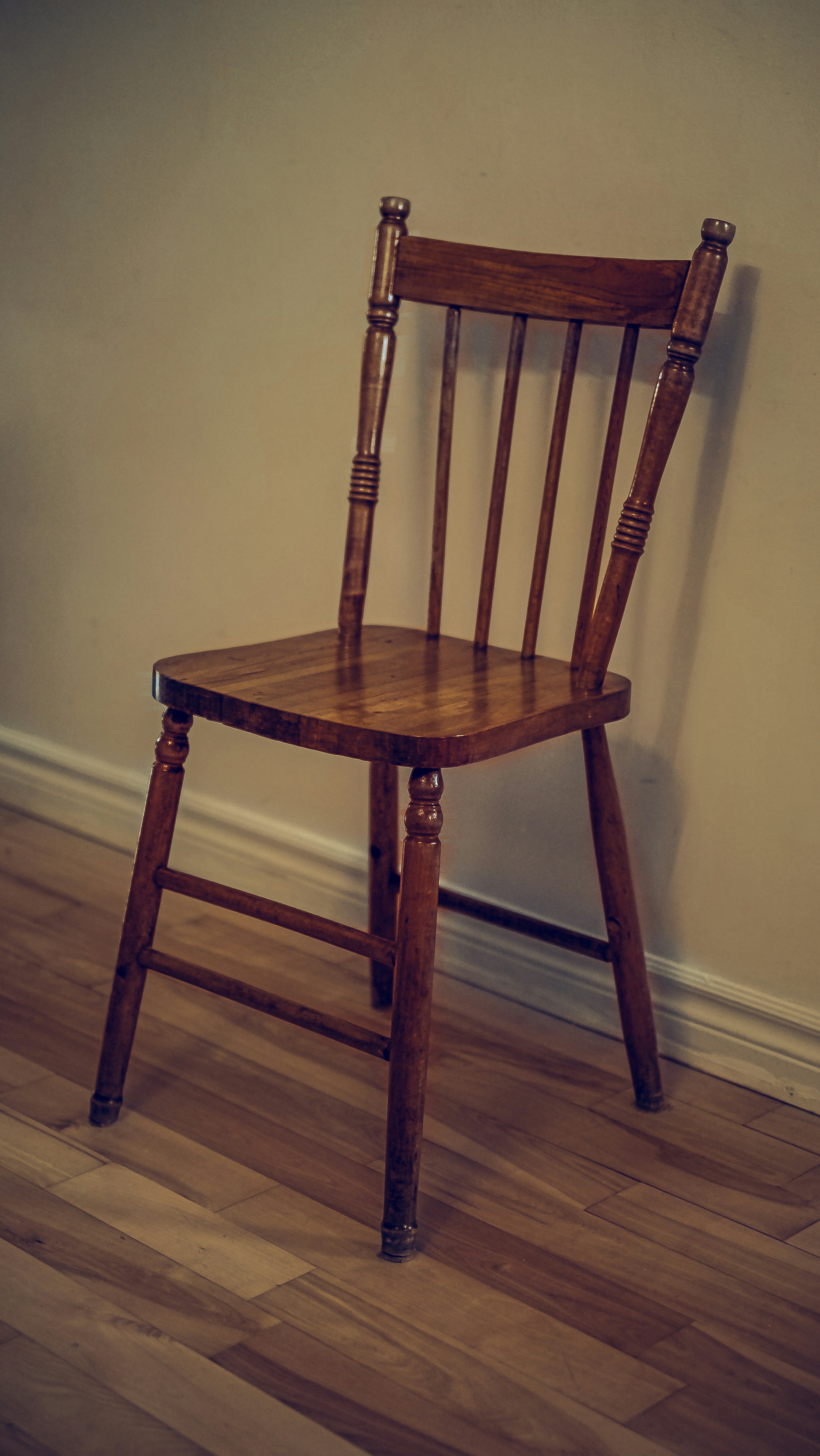 A vintage wooden chair with a simple yet elegant design, set against a neutral wall. The warm tones of the wood enhance its rustic charm.