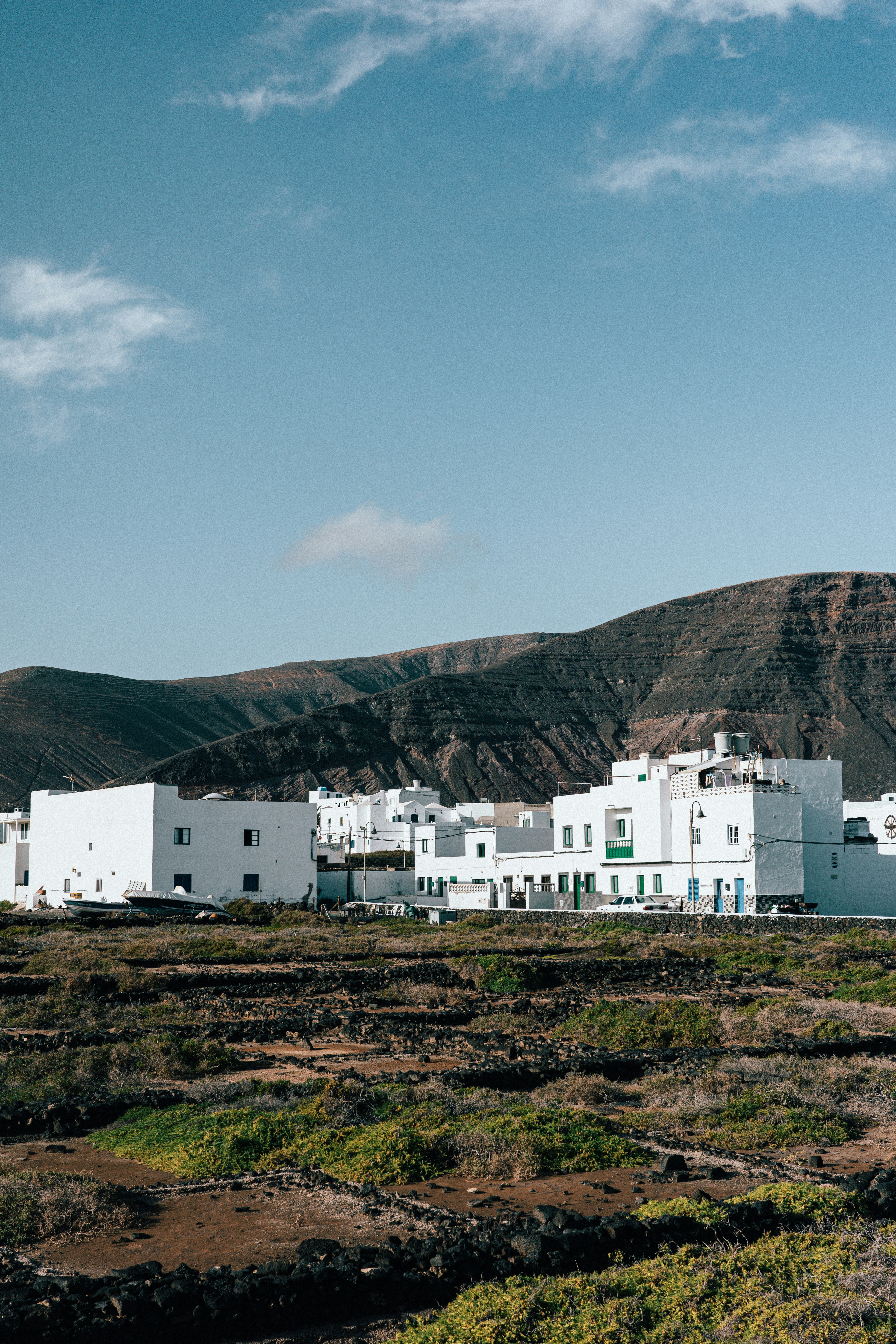 Whitewashed buildings nestled against a rugged mountain backdrop, surrounded by lush green fields and volcanic terrain.