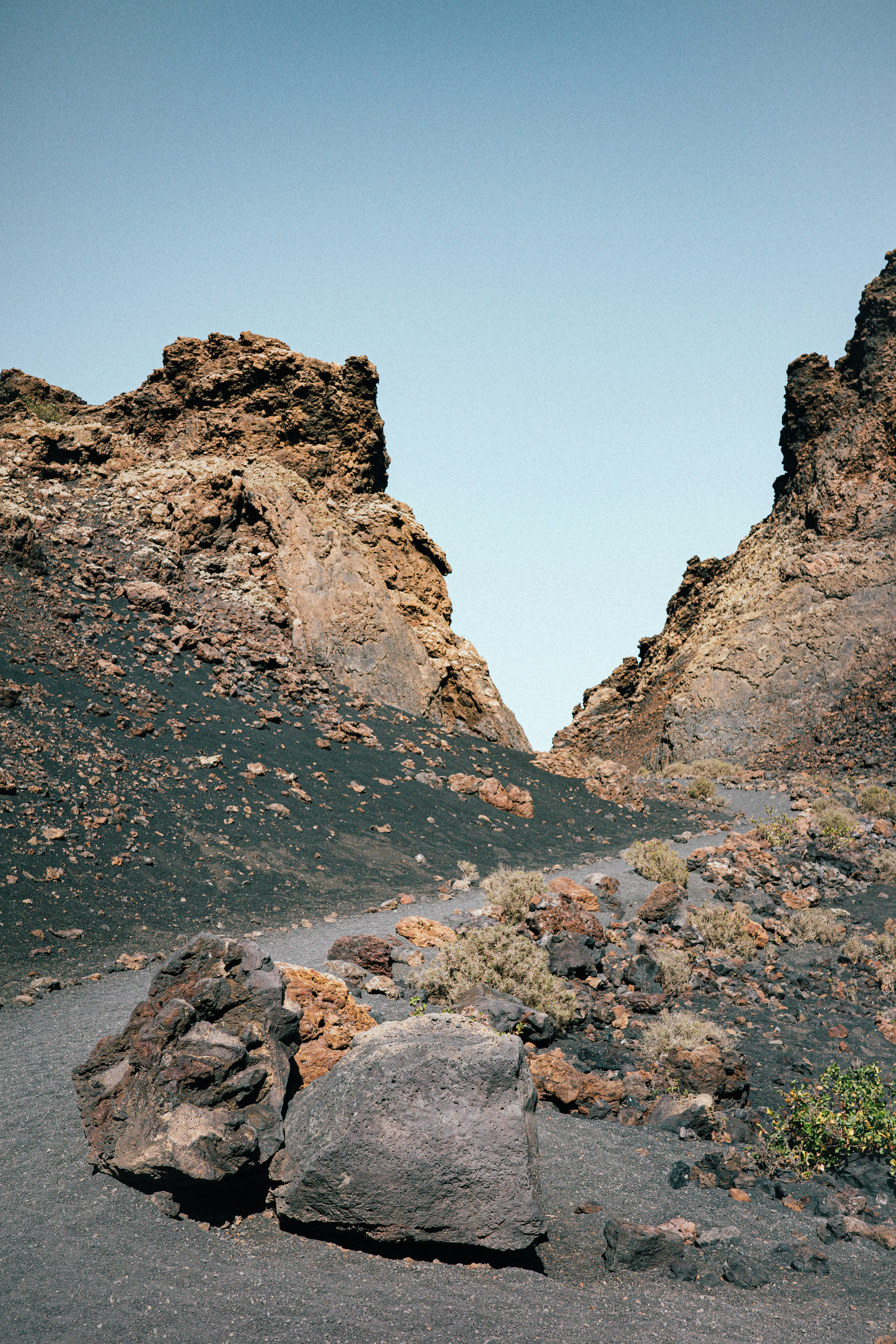 Jagged volcanic rock formations rise amidst a barren desert landscape under a clear blue sky.
