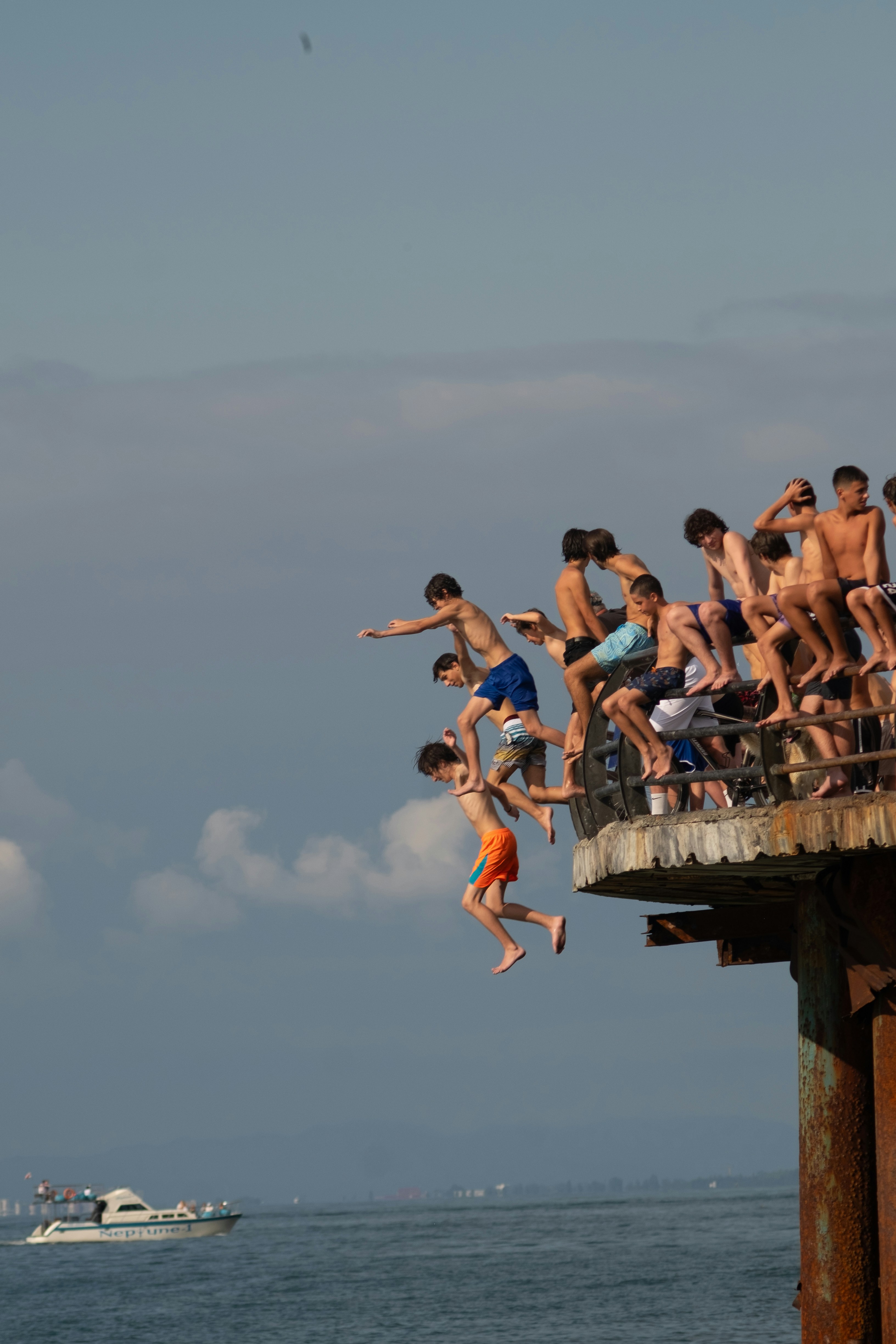 A group of people jumping off a pier into the water photo – Free Beach ...