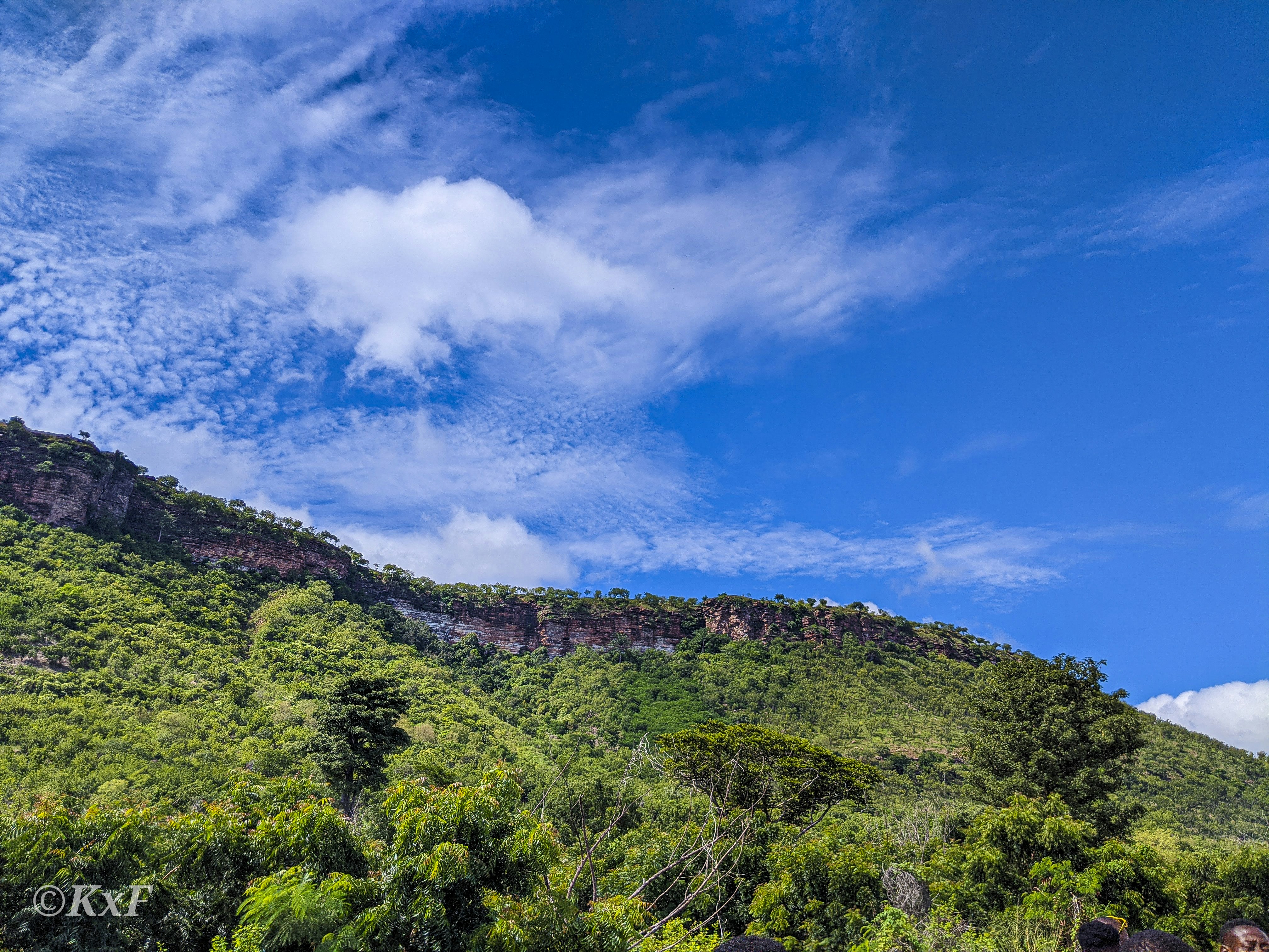 Lush green hillside beneath a bright blue sky with scattered clouds.
