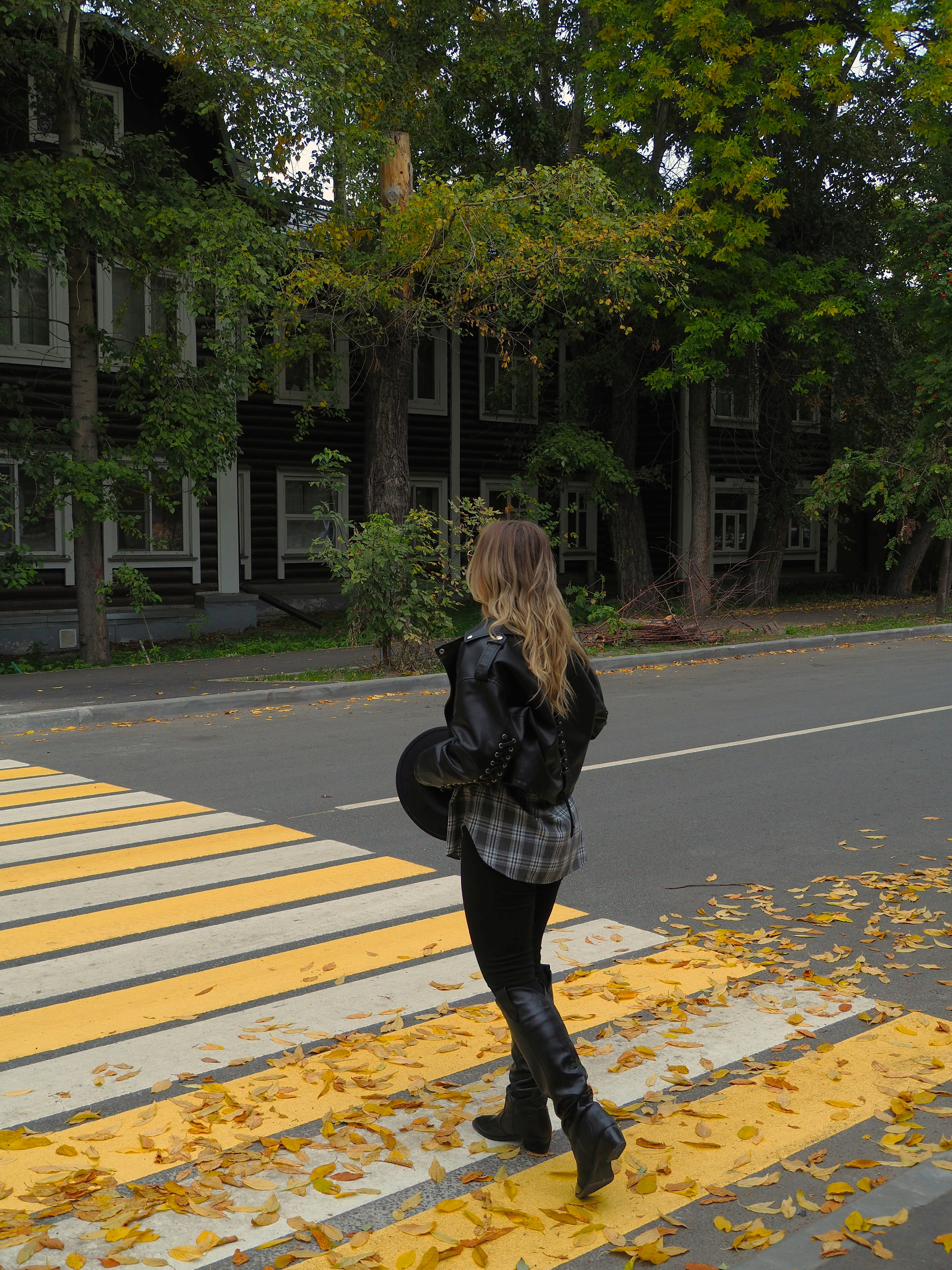 Autumn Crossing: A Woman in Black Boots at a Leaf-Strewn Crosswalk