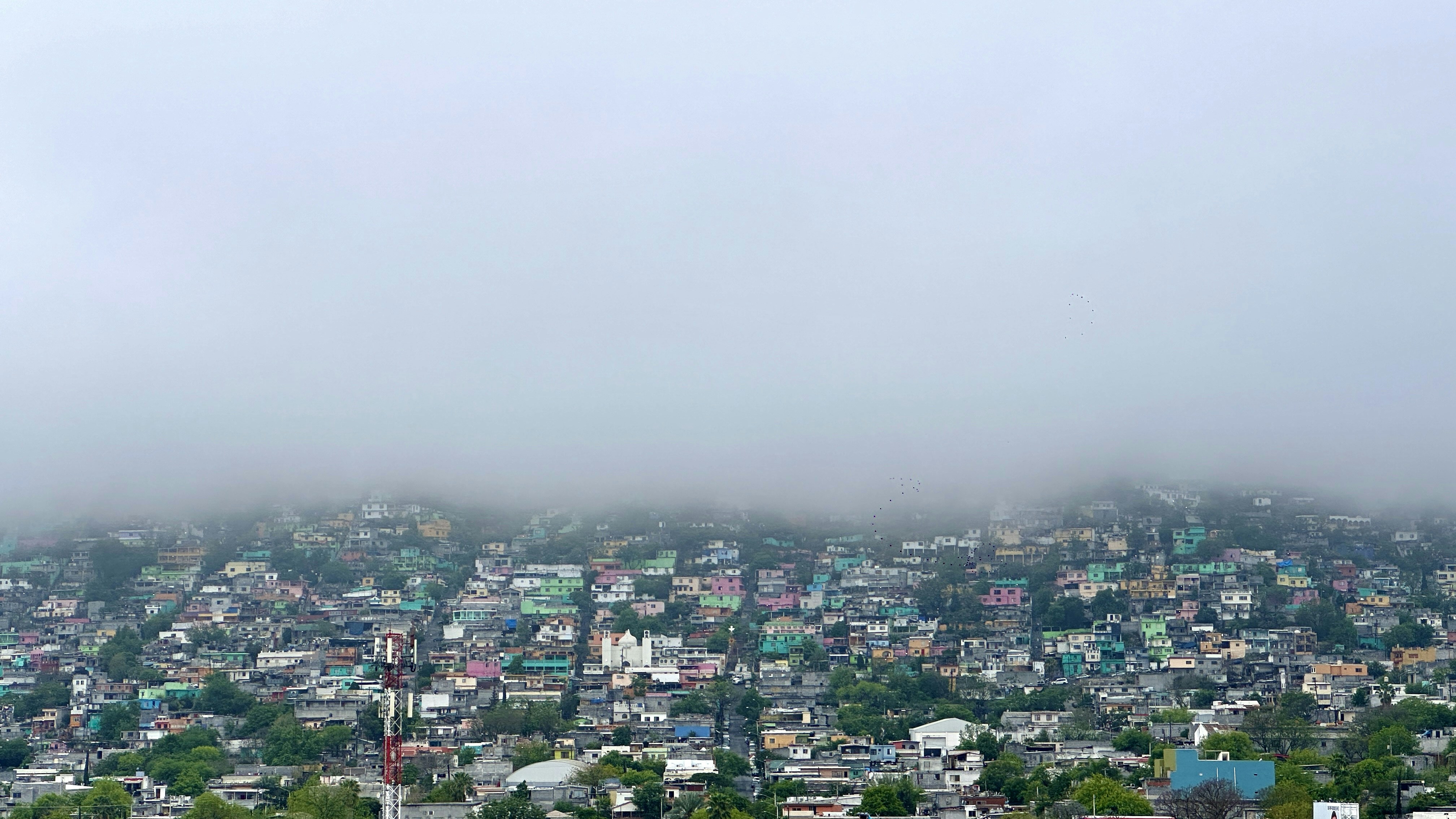 A vibrant hillside community shrouded in fog, revealing a patchwork of colorful houses. The atmosphere hints at a tranquil yet mysterious environment.