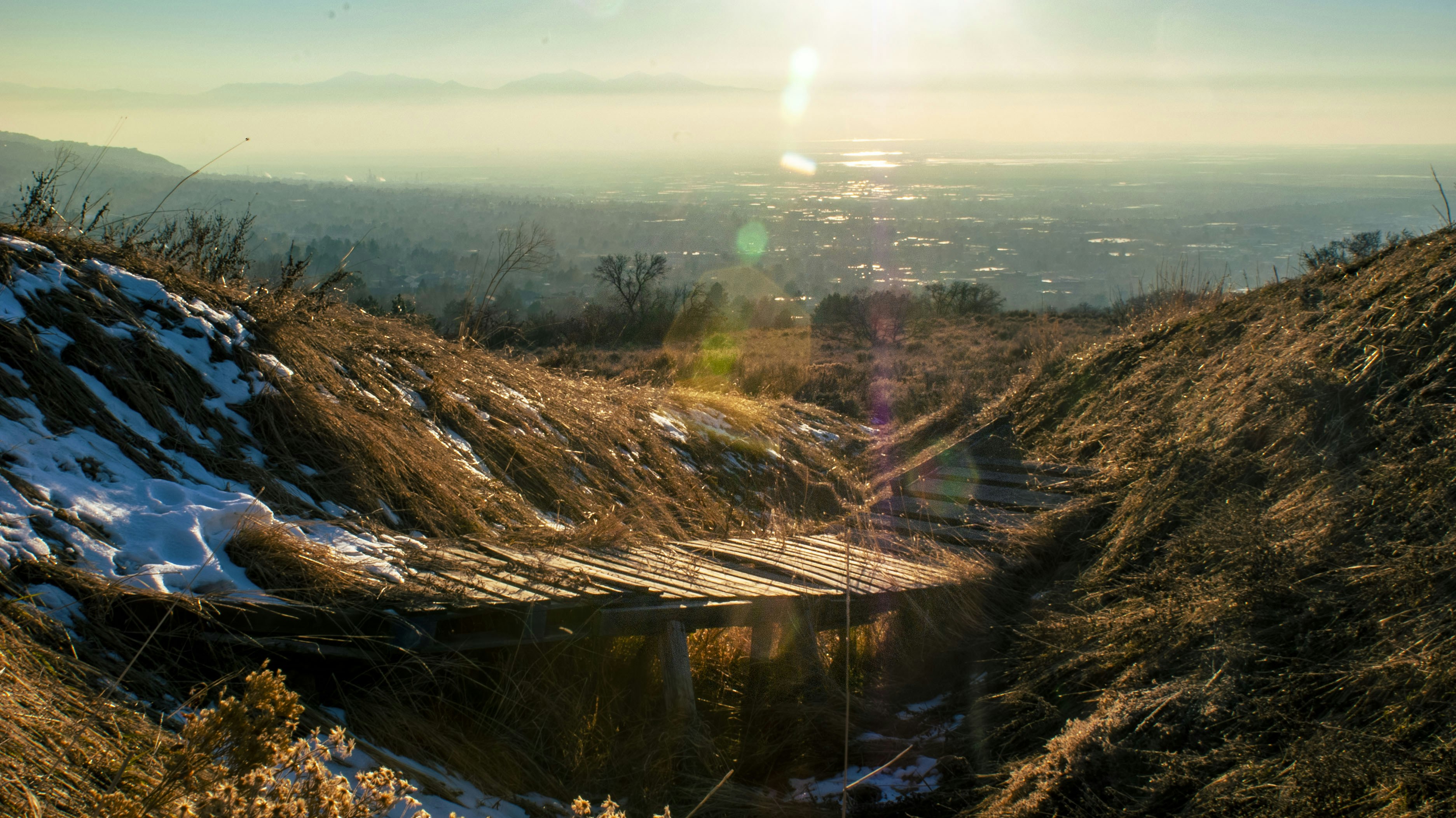 Sunlit valley with patches of snow and grass under a clear sky.