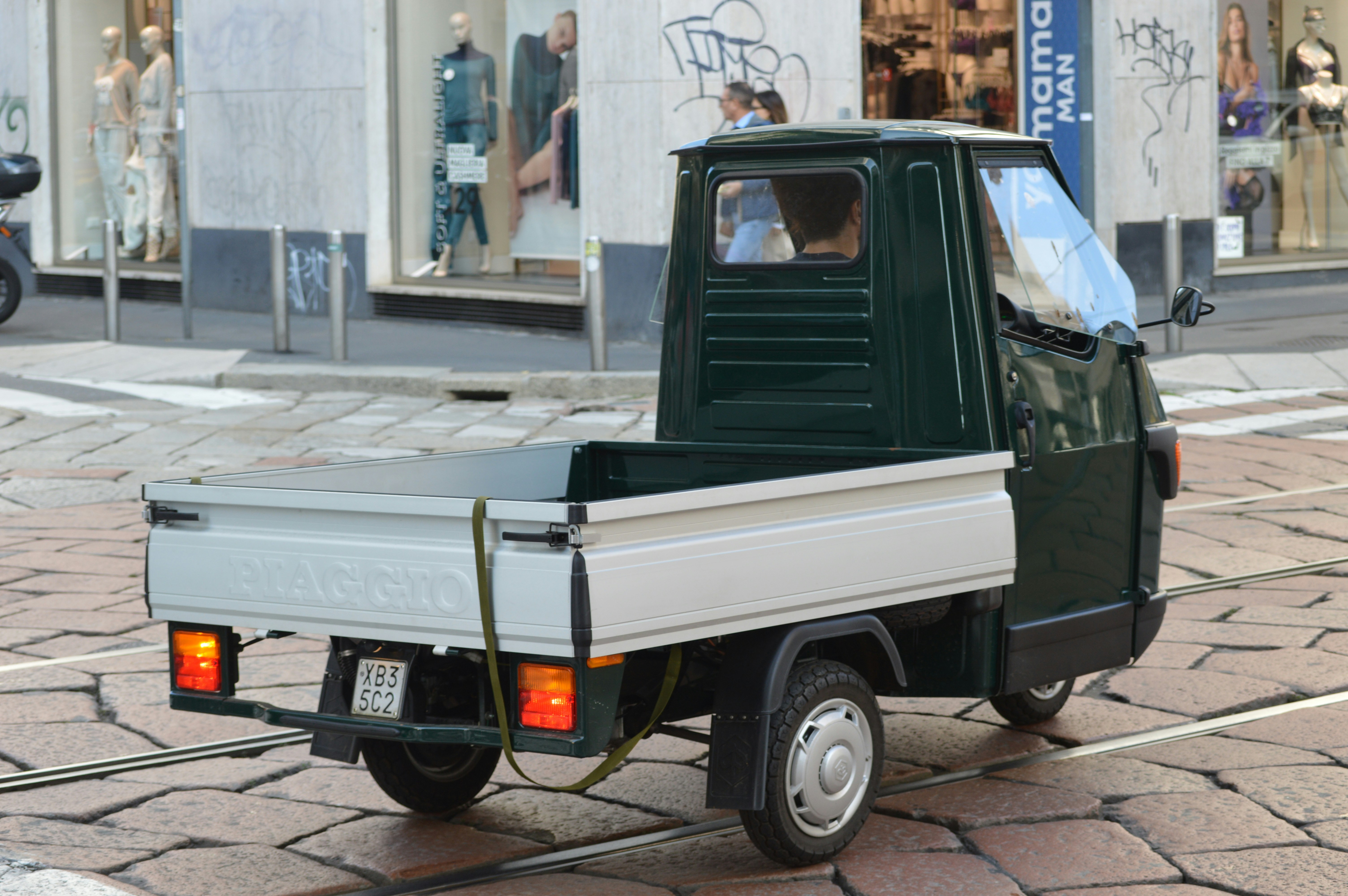 Green utility micro-truck stalls on a cobbled city plaza