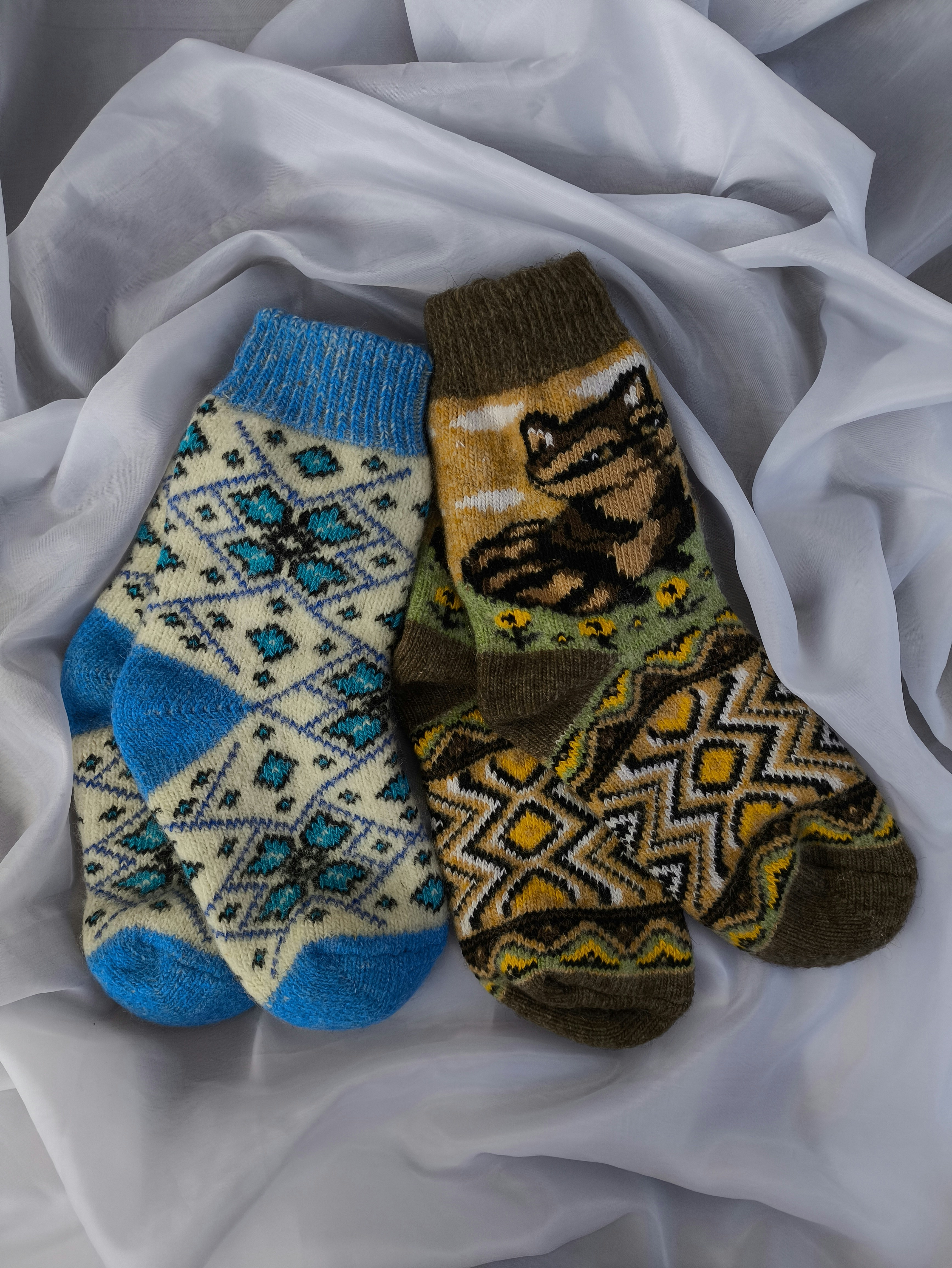 Pair of colorful knitted socks resting on soft fabric, featuring intricate patterns and a playful cat design. Perfect for adding charm to winter attire.