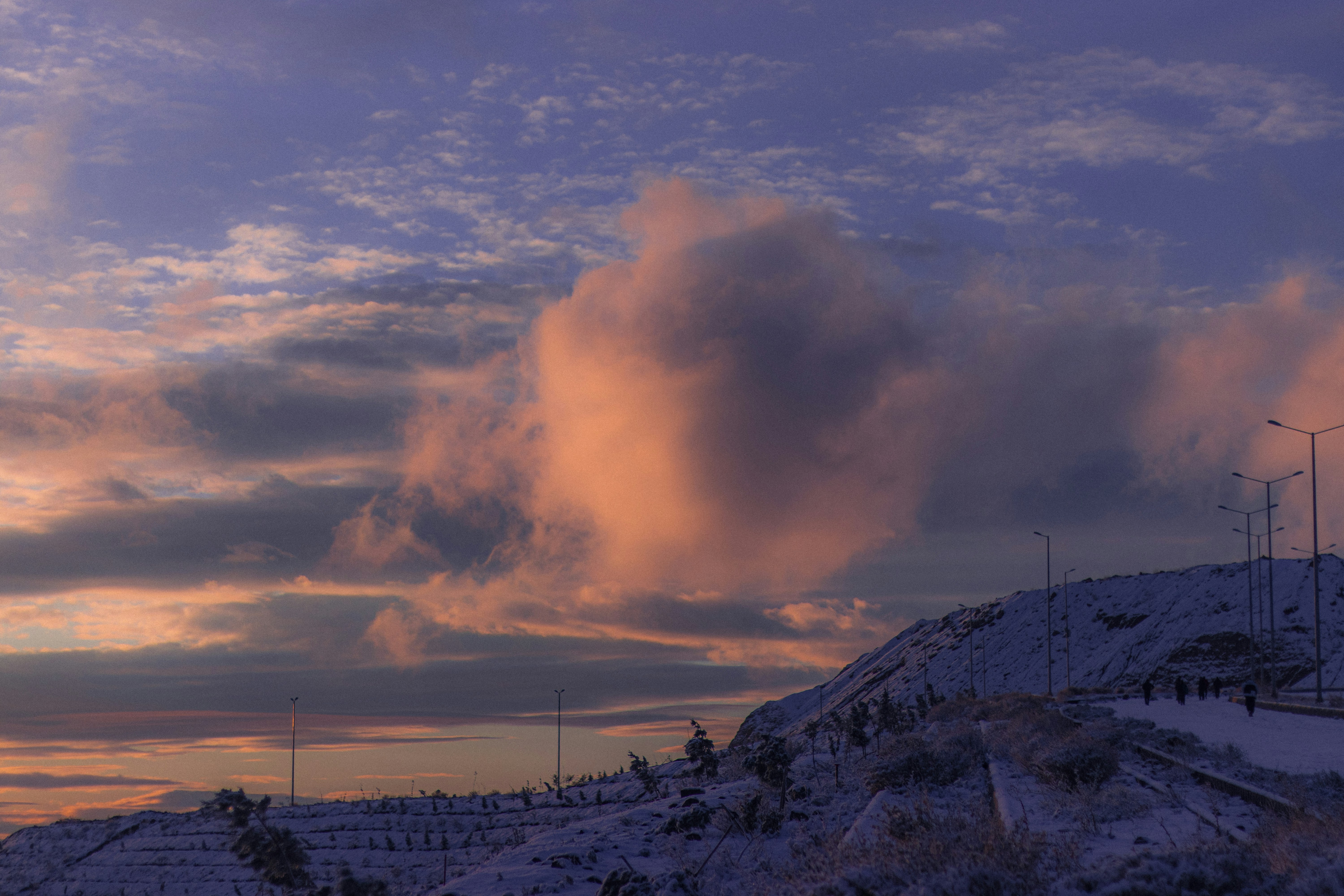 Vibrant clouds illuminated by sunset over a snow-covered hillside with silhouetted trees.