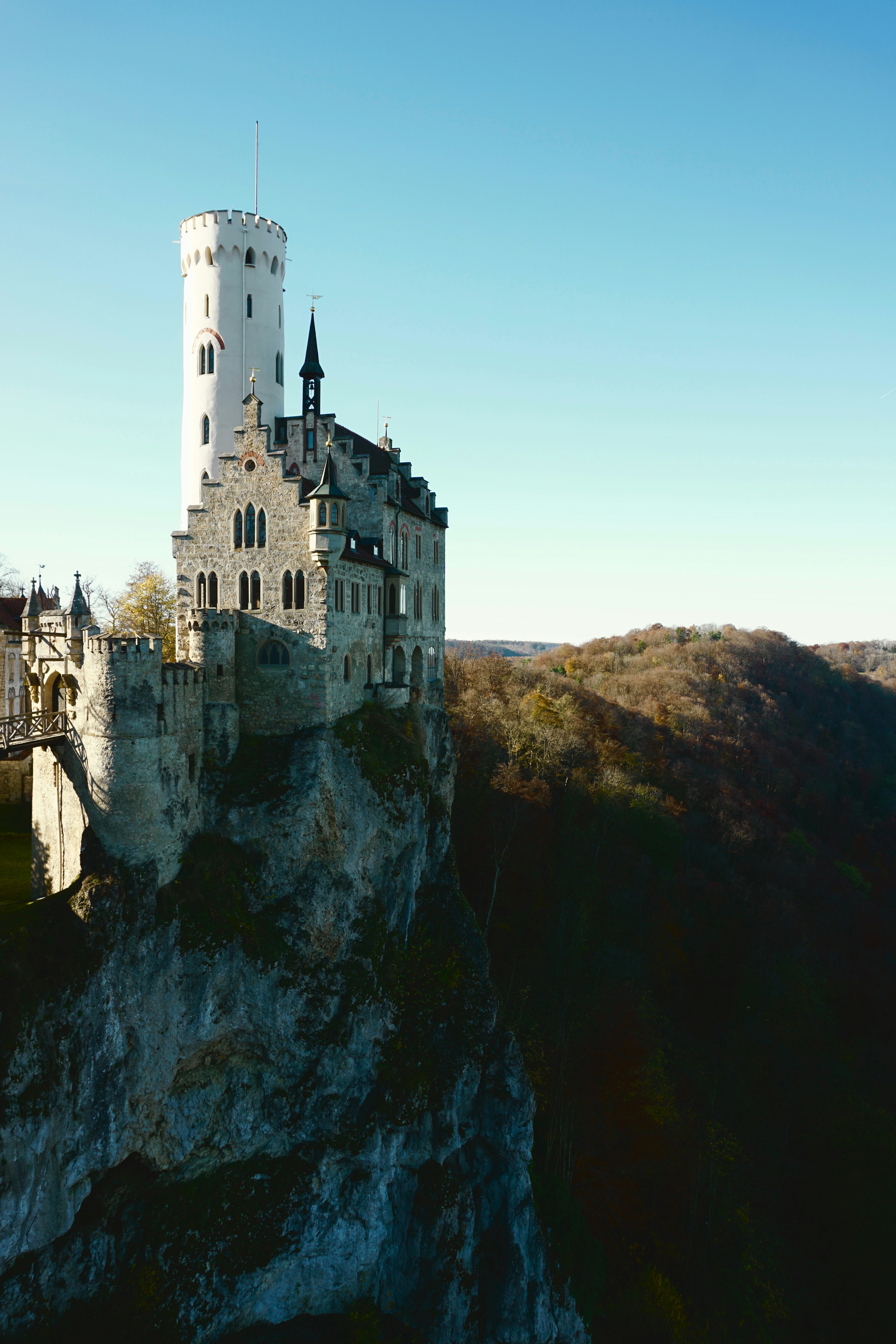 A historic castle perched dramatically on a cliff, surrounded by autumn foliage and clear blue skies.