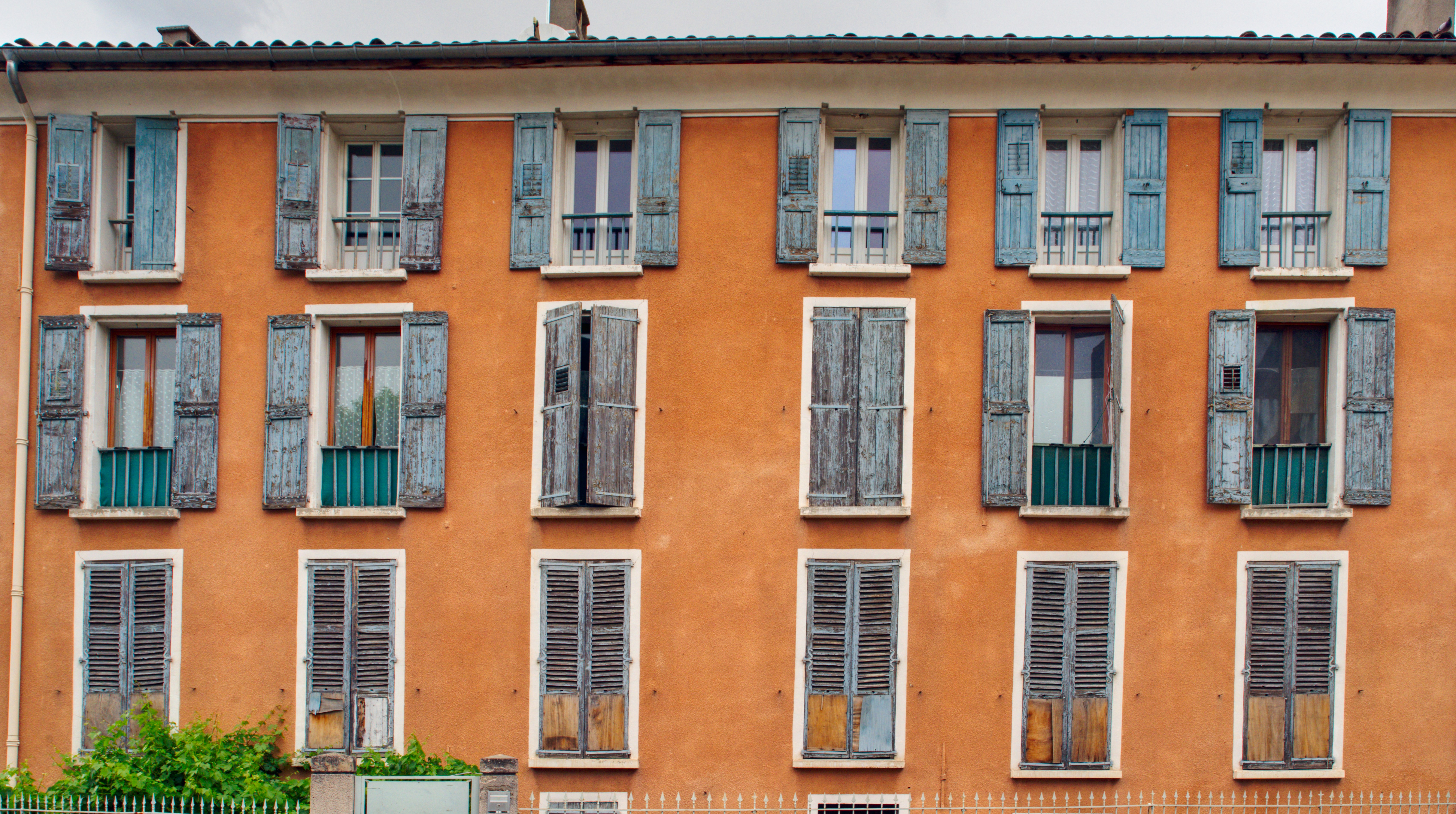 Charming orange building with blue shutters and wooden window frames, showcasing a blend of rustic architecture and fading elegance.