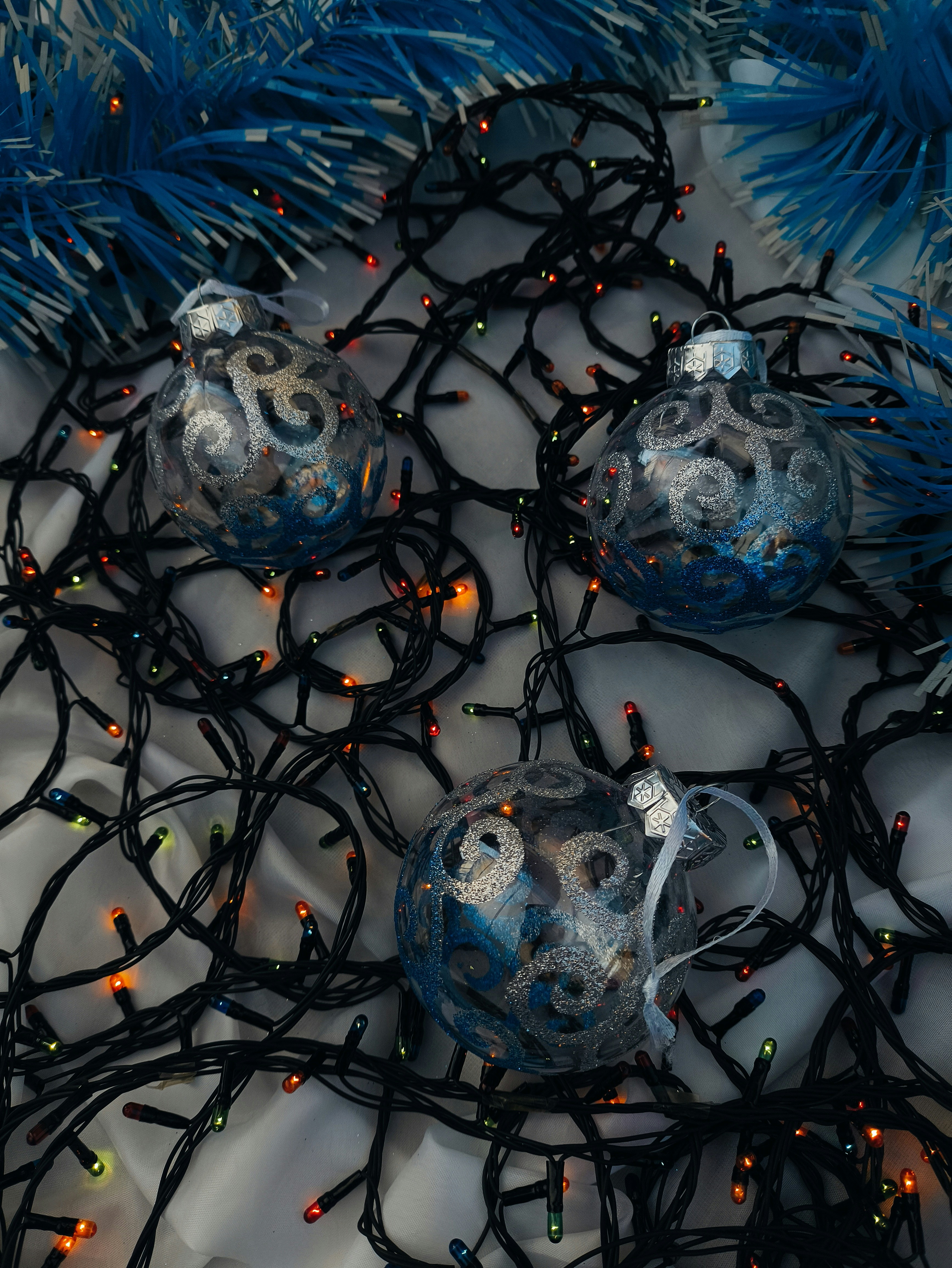 Three frosted blue glass ornaments sit among a tangle of black string lights with tiny colored bulbs.