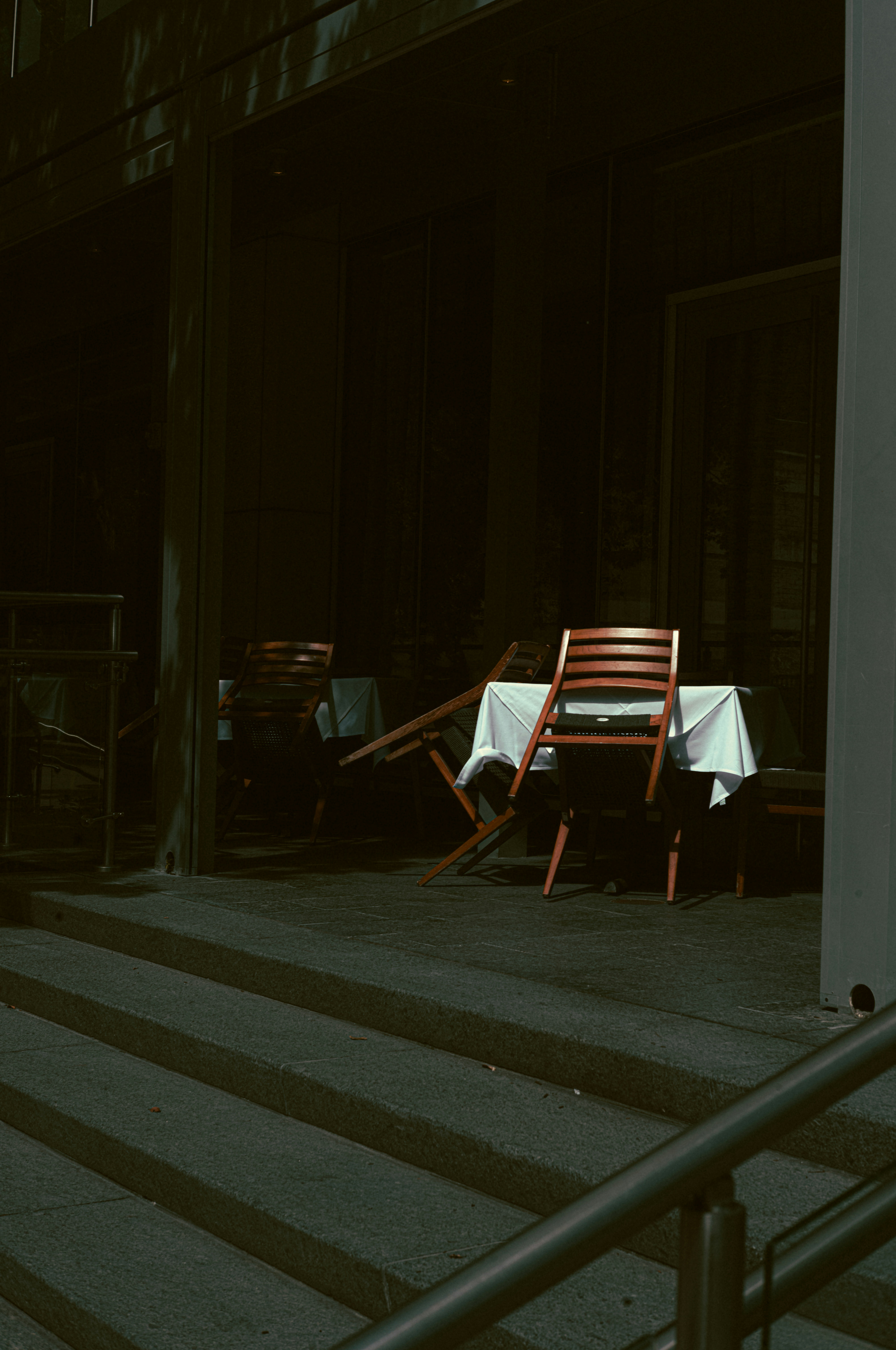 Empty café terrace with scattered chairs and a lone table, evoking a sense of solitude and quietude. The play of shadows adds depth to the scene.