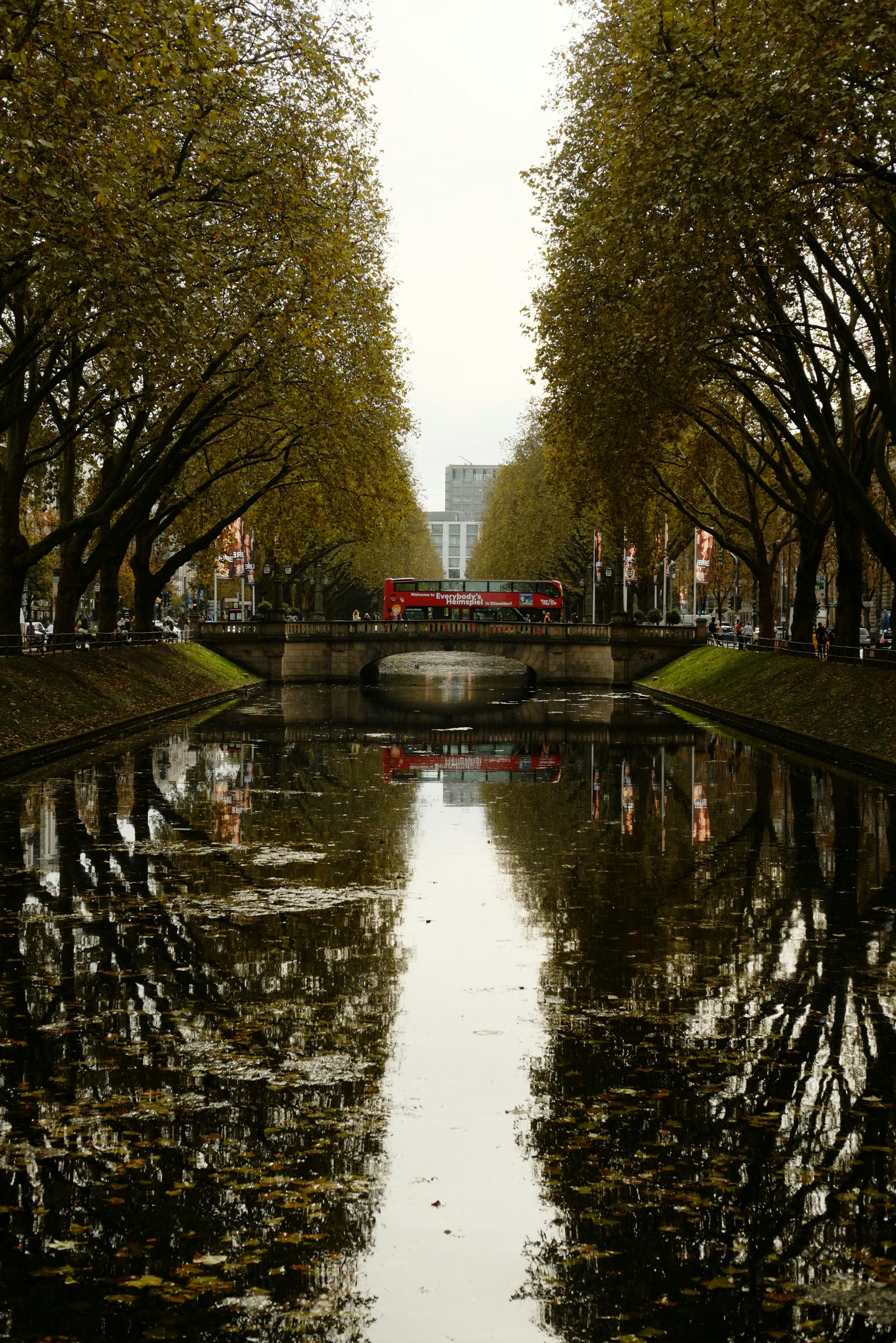 Crimson Bus on a Canal Bridge Framed by Autumn Trees
