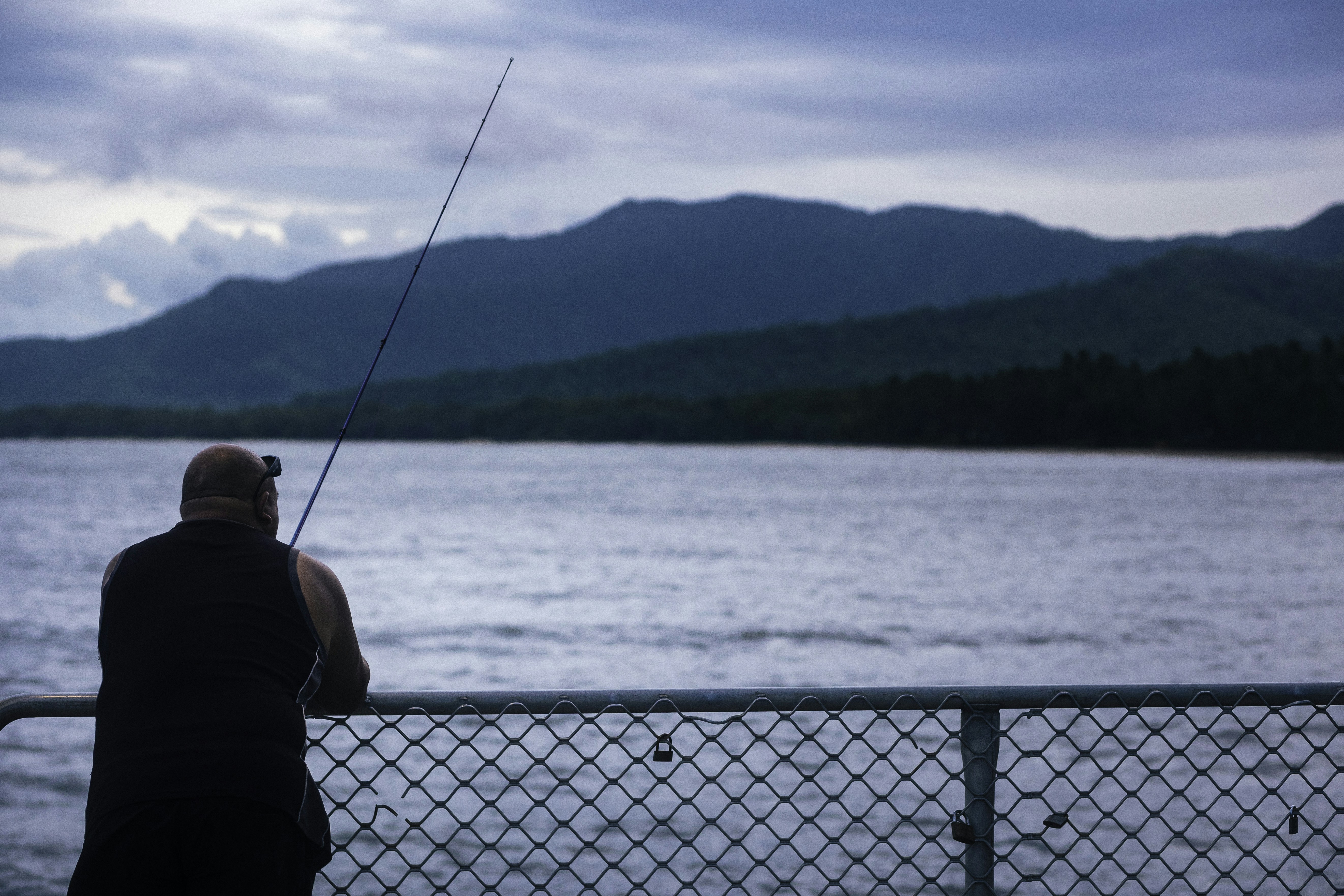 Lone Angler at the Rail: Quiet Blue Lake Under Distant Peaks