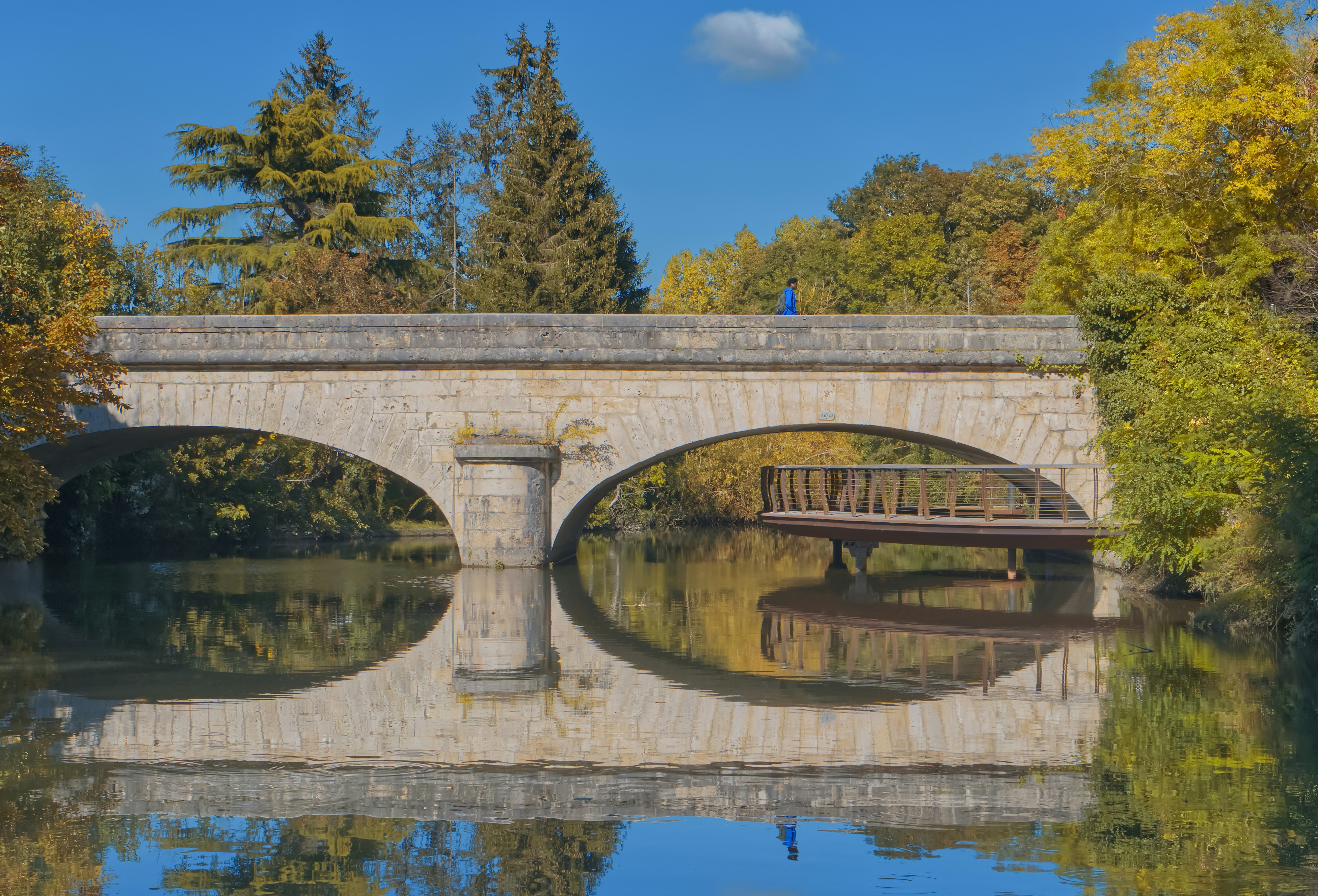 🎶🎶🎶 Il suffit de passer le pont, c’est tout de suite l’aventure 🎶🎶🎶. | A bridge over a body of water surrounded by trees