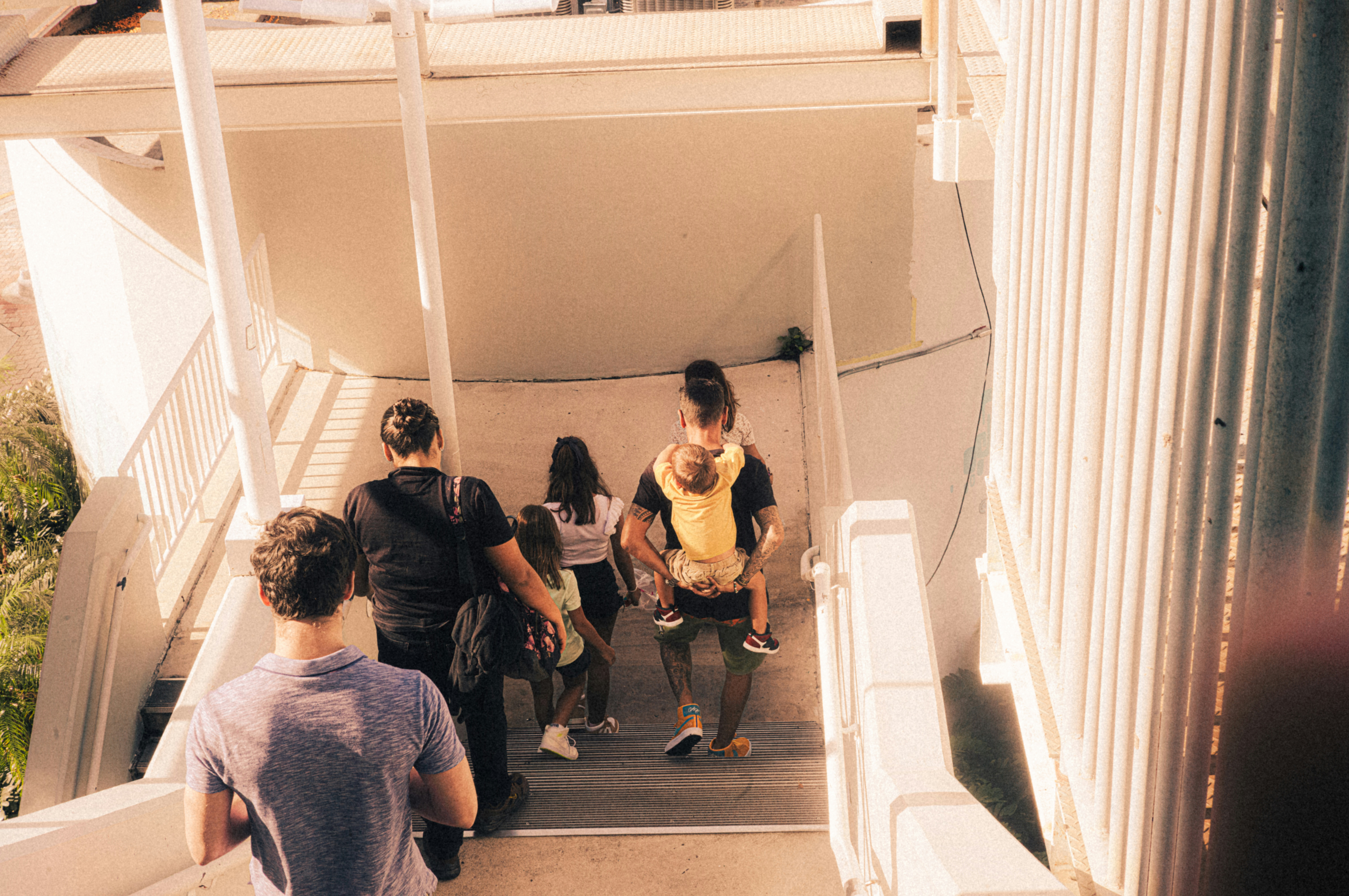 Candid photograph of a group descending a sunlit stairwell, captured from above as they move toward the lower level.