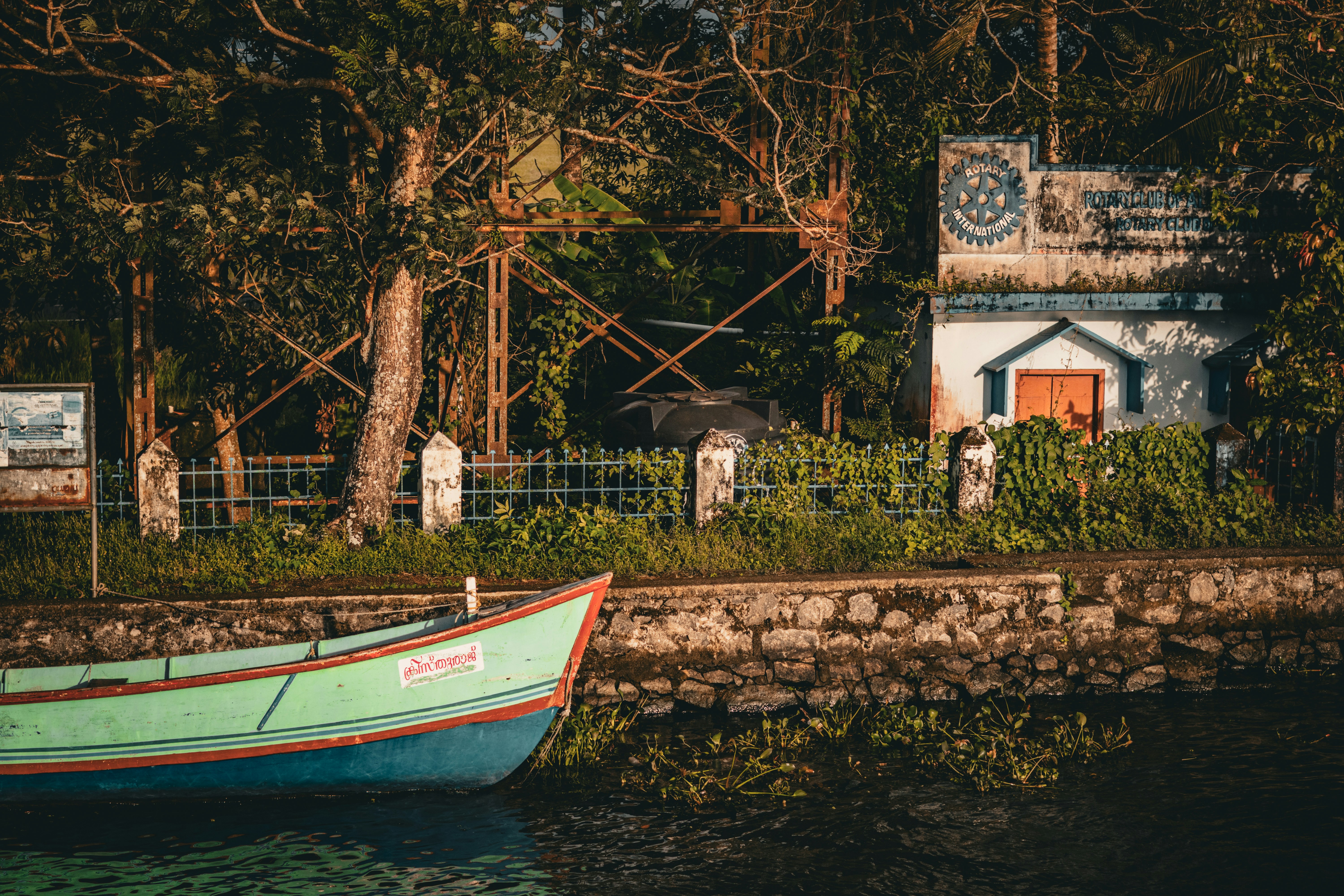 Wooden boat moored by a rustic riverside cabin enveloped in lush greenery and warm evening light.