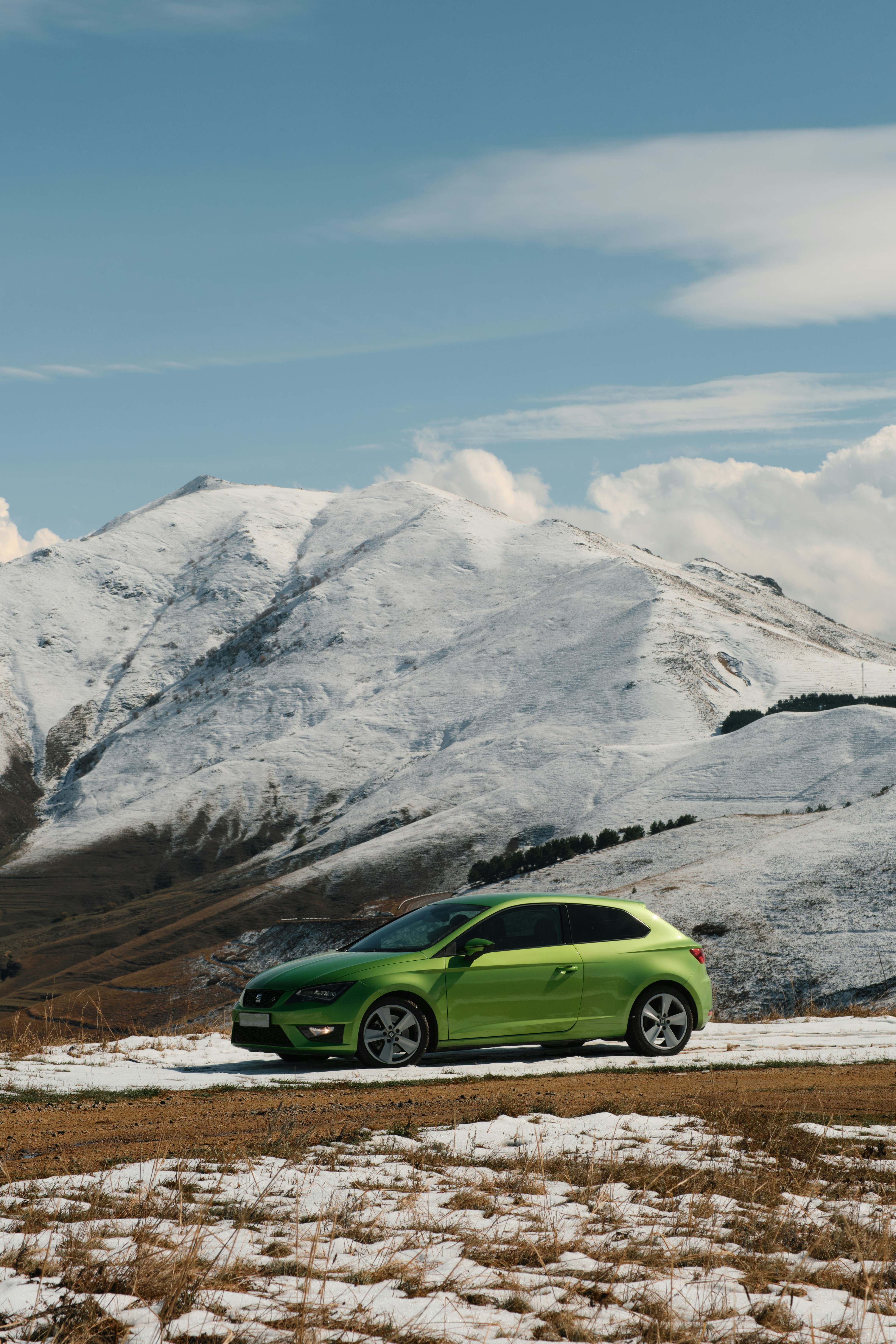 Verdant Accent in Alpine White: Lime Hatchback Amid Snowy Peaks