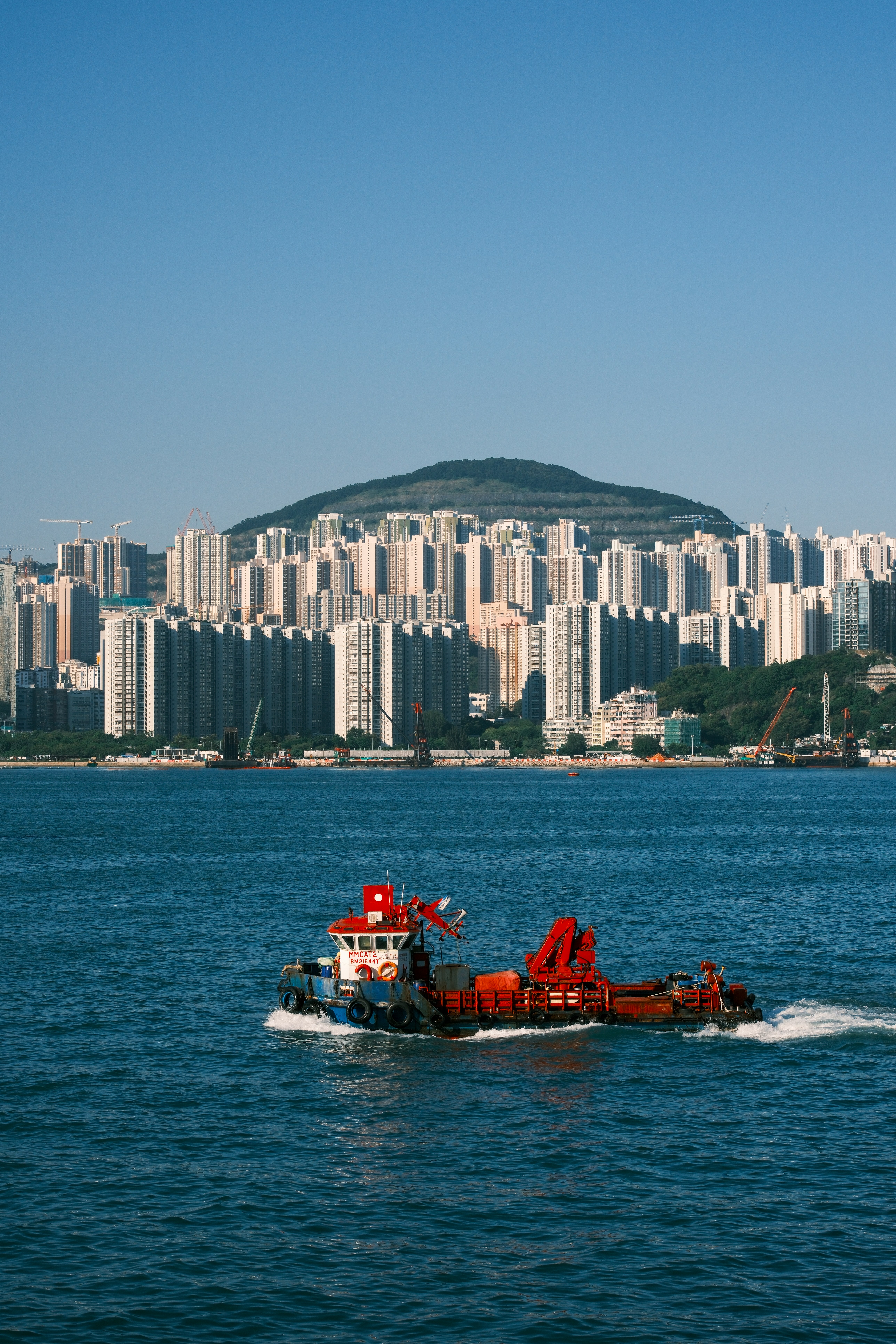 Red Tug at the Waterfront: A Harbor Scene Framed by Towers and a Green Hill