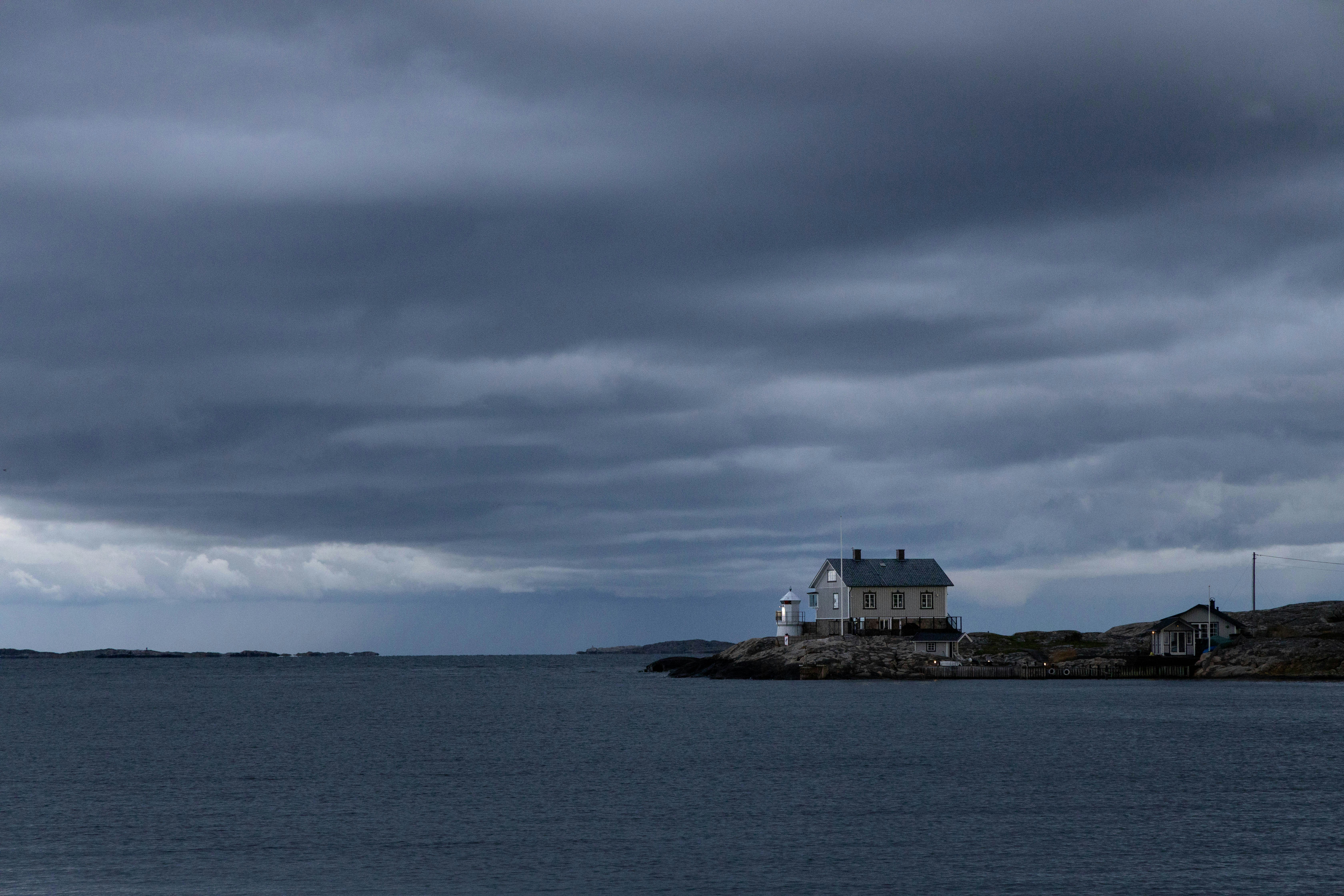 A lone lighthouse and house perched on a rocky shoreline beneath dramatic, overcast clouds.