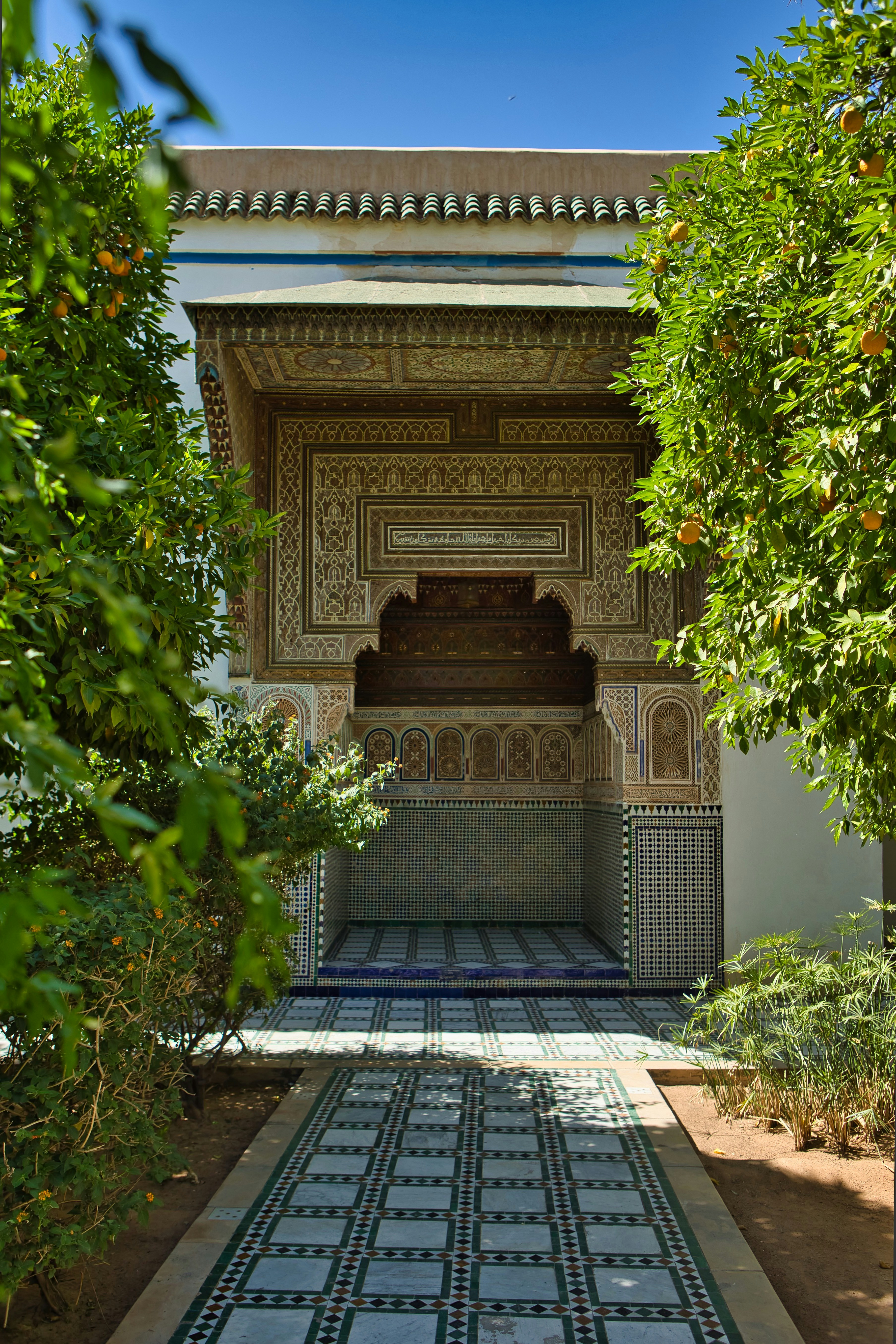 Intricate architectural detail of a Moroccan courtyard framed by lush greenery and vibrant orange trees.