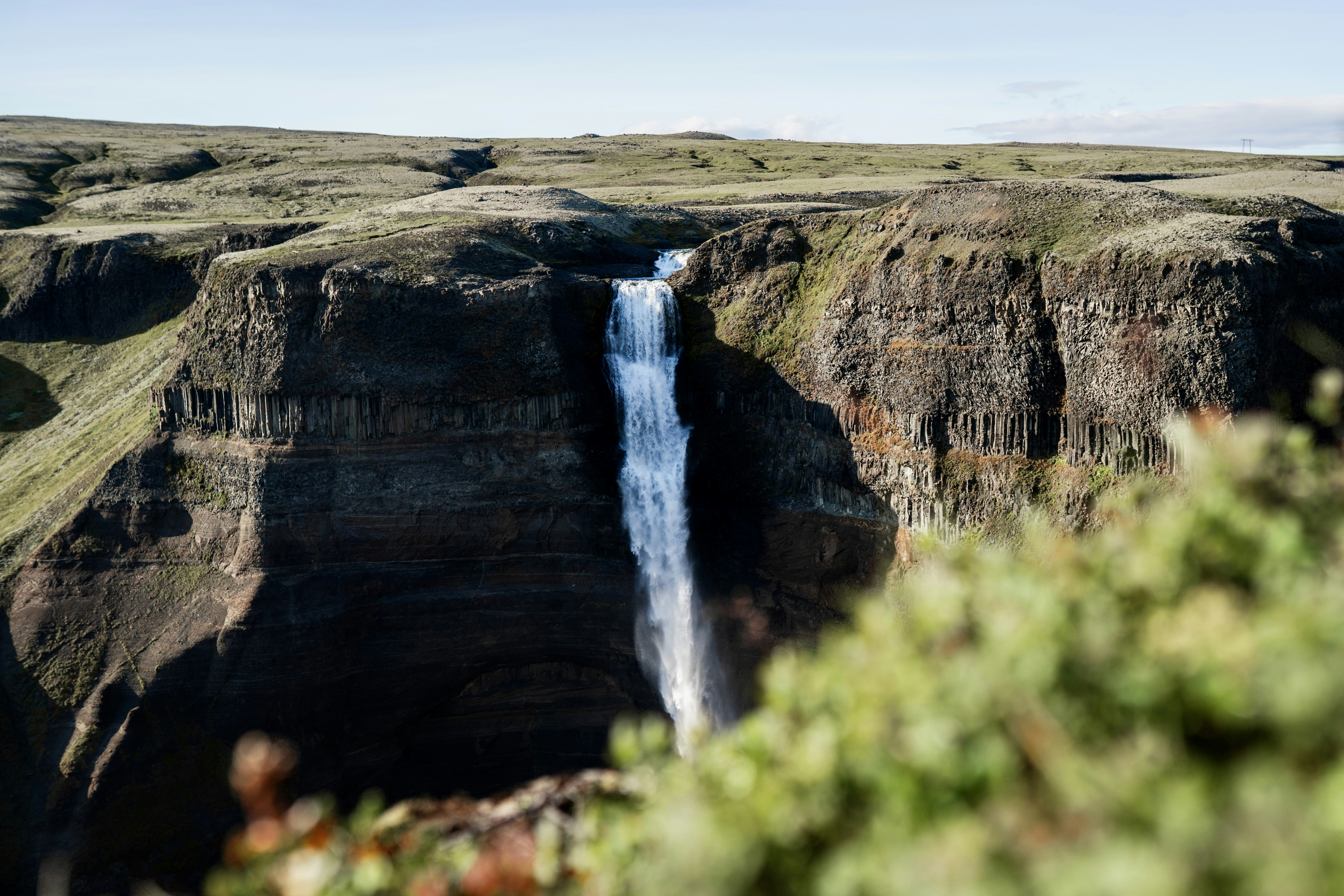 Waterfall plunging between rugged cliffs surrounded by green highlands.