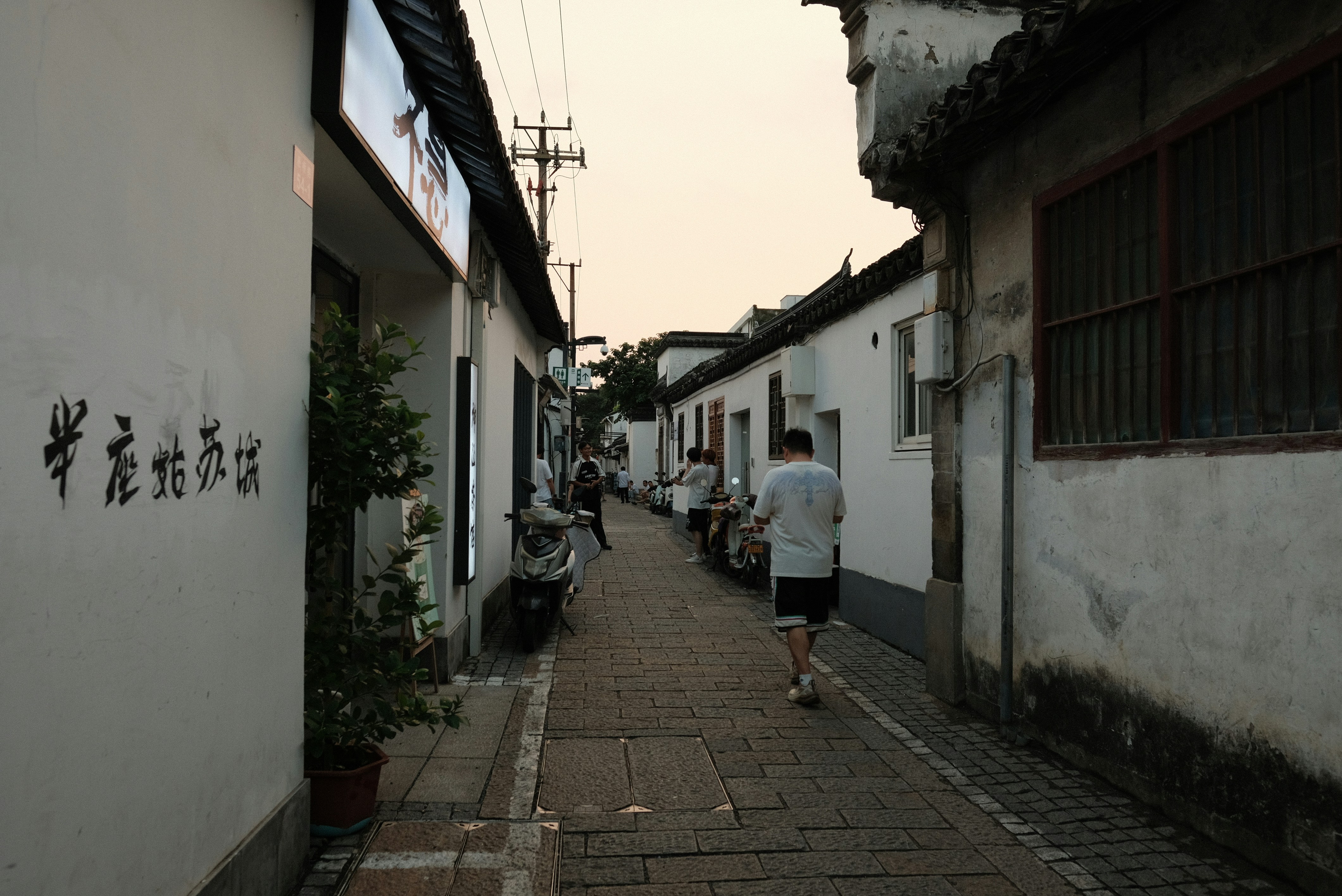 Dusk in a Whitewashed Alley: A solitary figure threads the lantern-lit lane