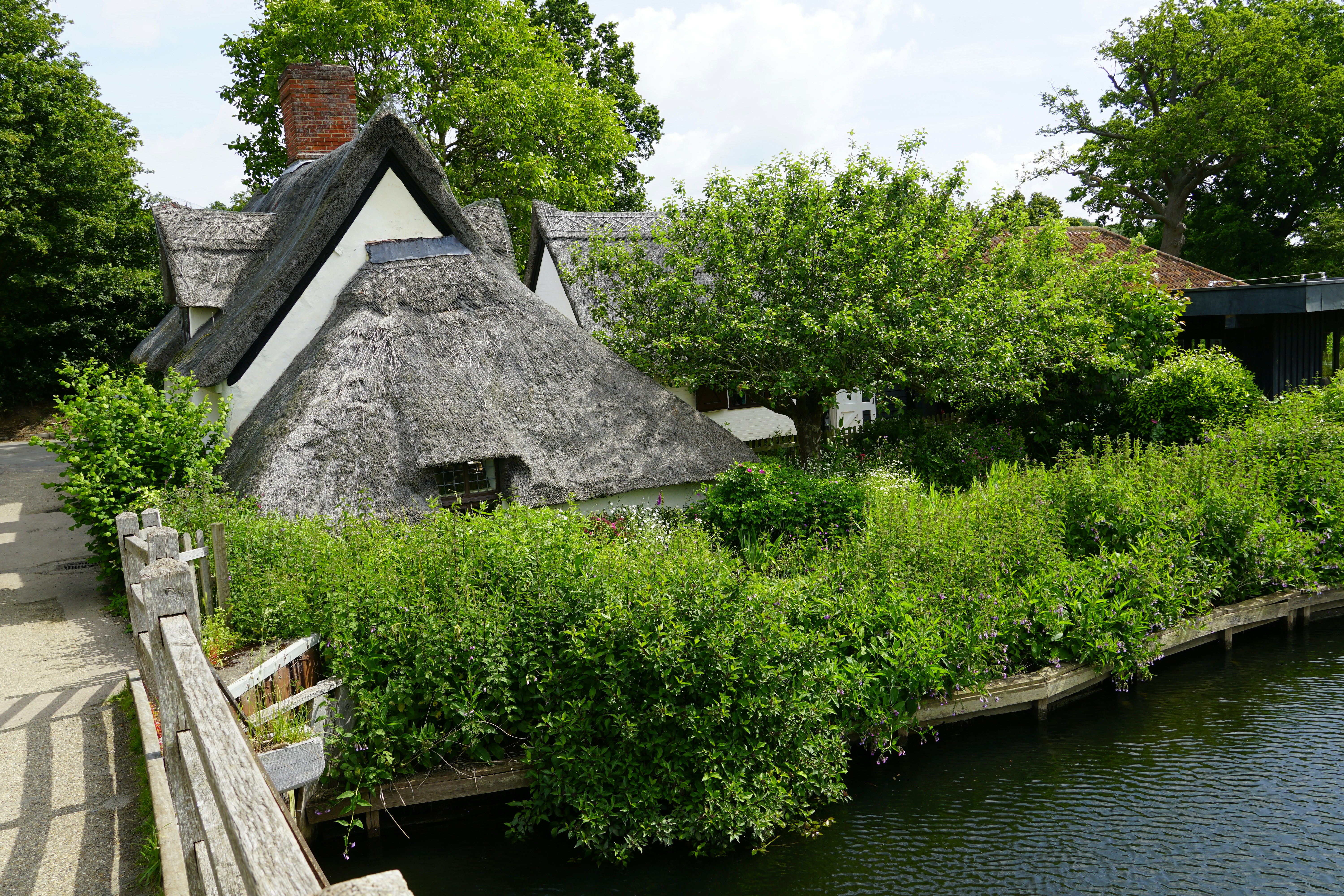 Thatched cottage nestled by a lush, green riverside under a clear sky.