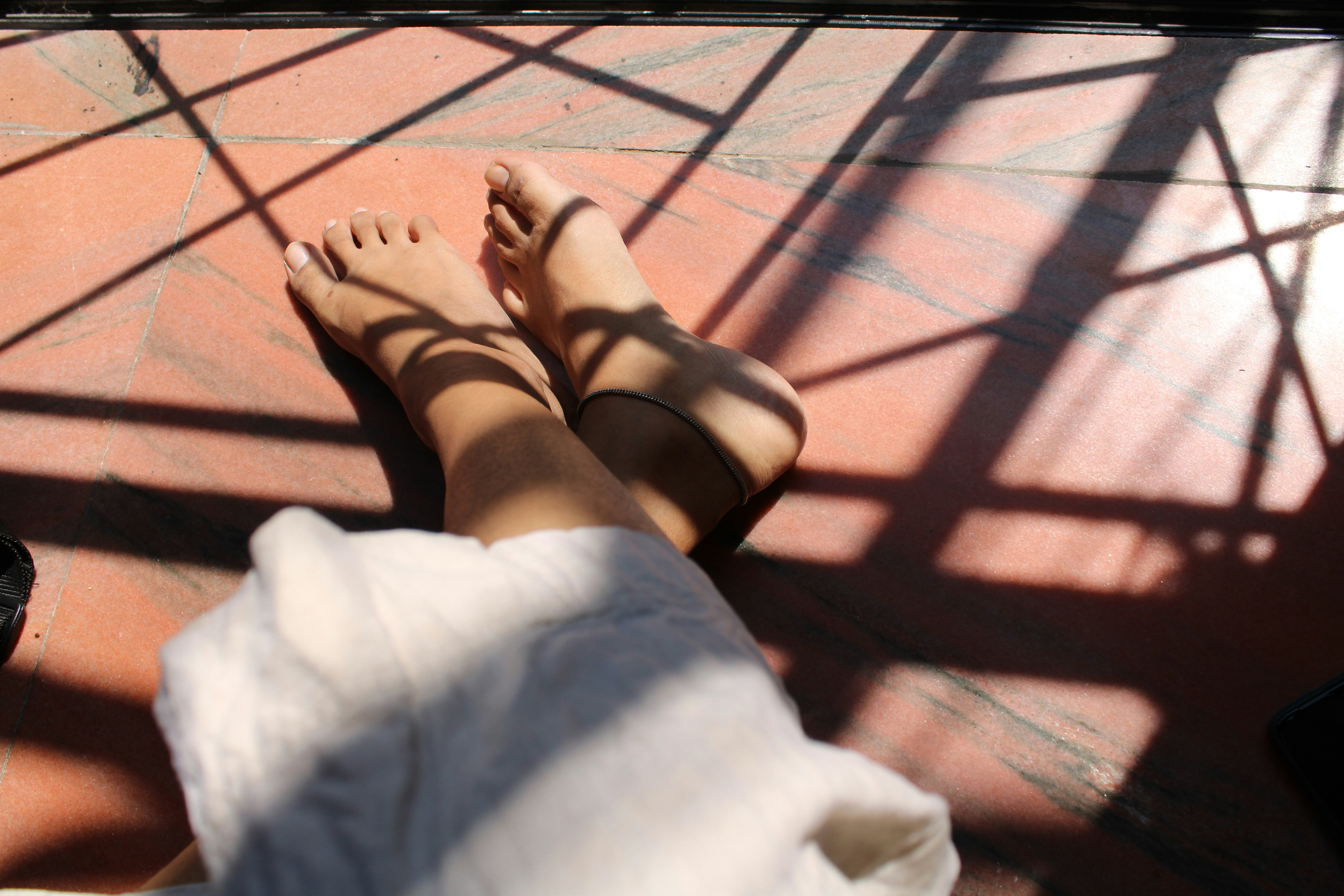 Sun-dappled Terrace: Bare Feet, White Cloth, and Crisscross Shadows