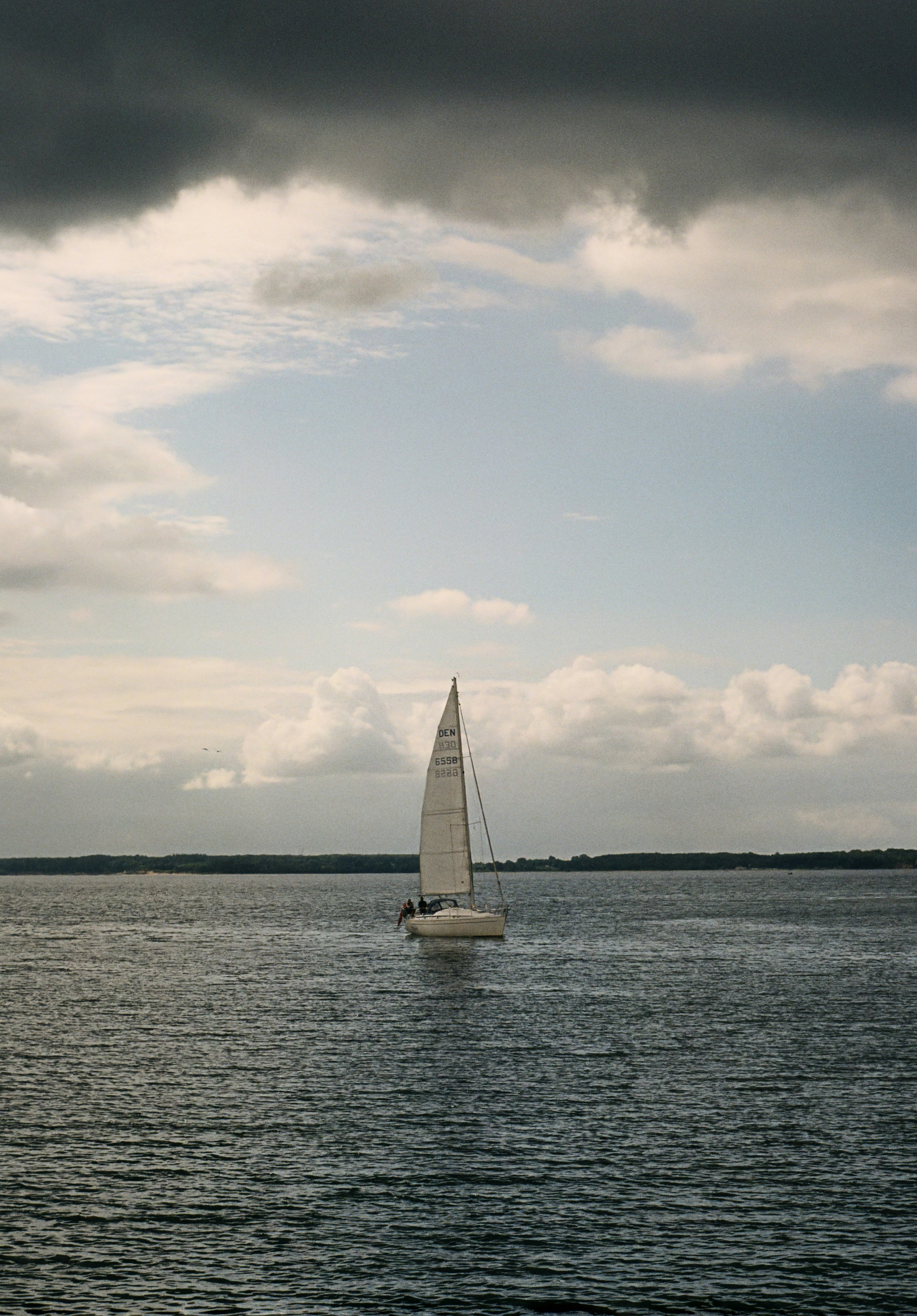 Sailboat gliding across a calm sea under a sky filled with dramatic clouds.