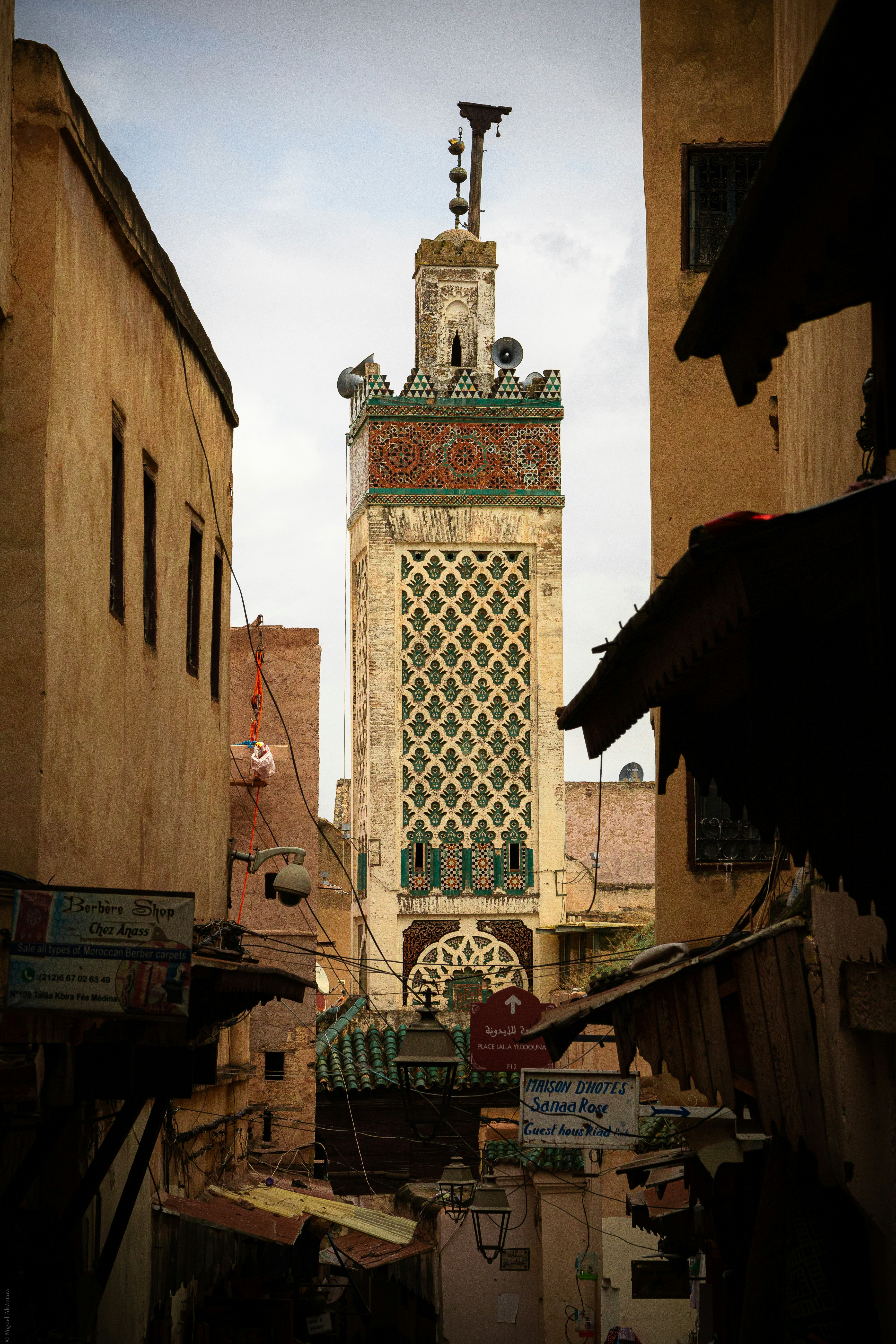 Intricate minaret rises above narrow alleyway, adorned with vibrant tile work and surrounded by historic architecture.
