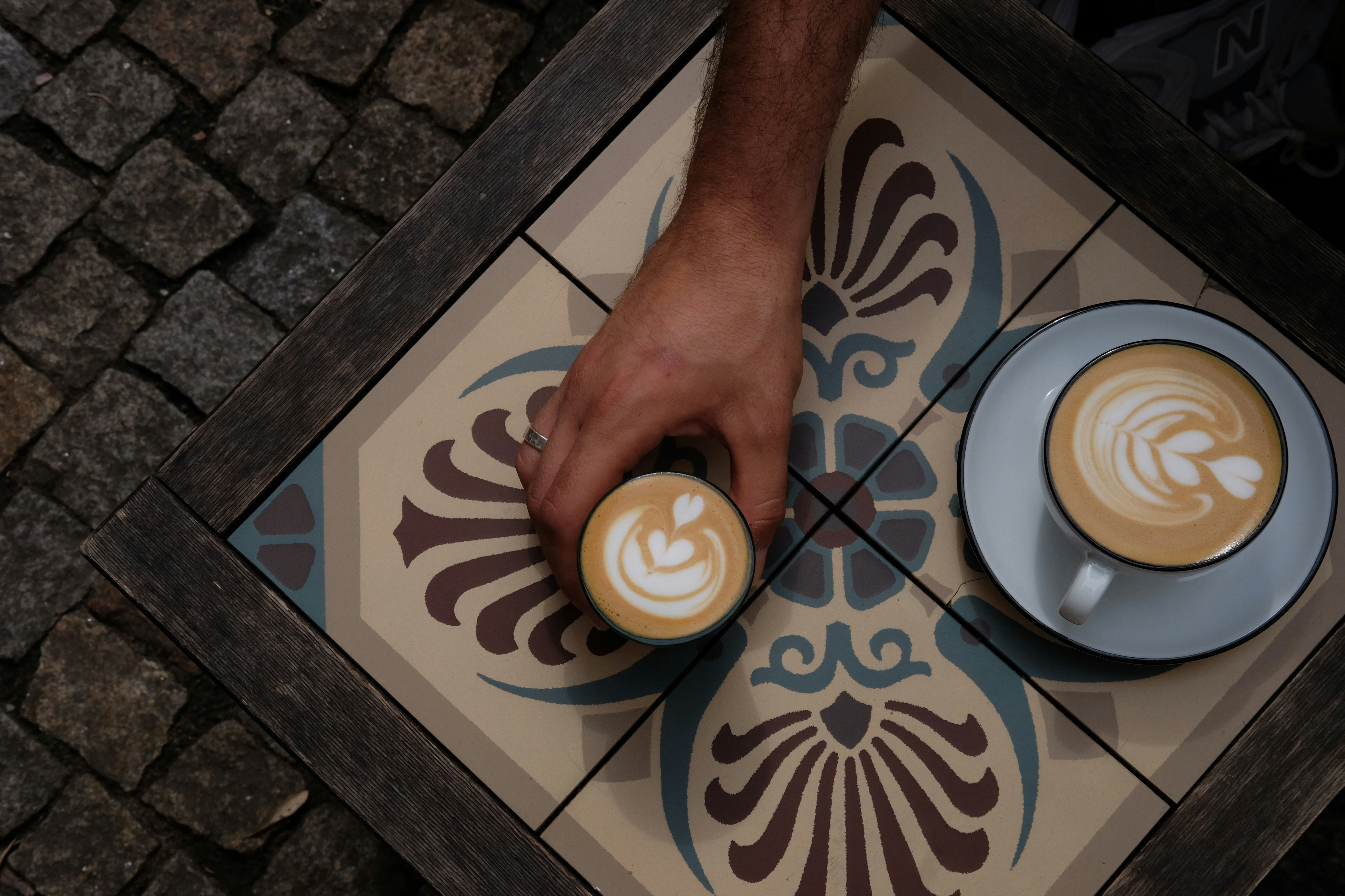 Latte Mosaic: A Hand Grips the Cup on Tile-Crafted Table