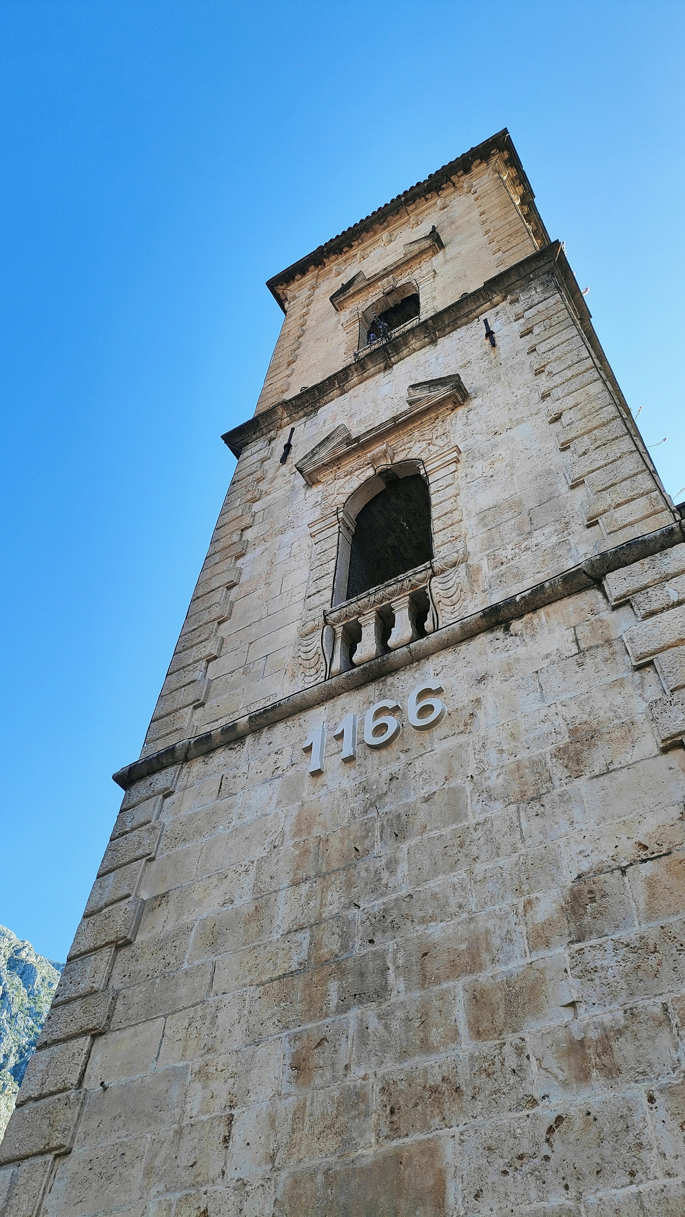 Historic stone tower with a prominent number '1166' engraved on its facade, set against a clear blue sky.