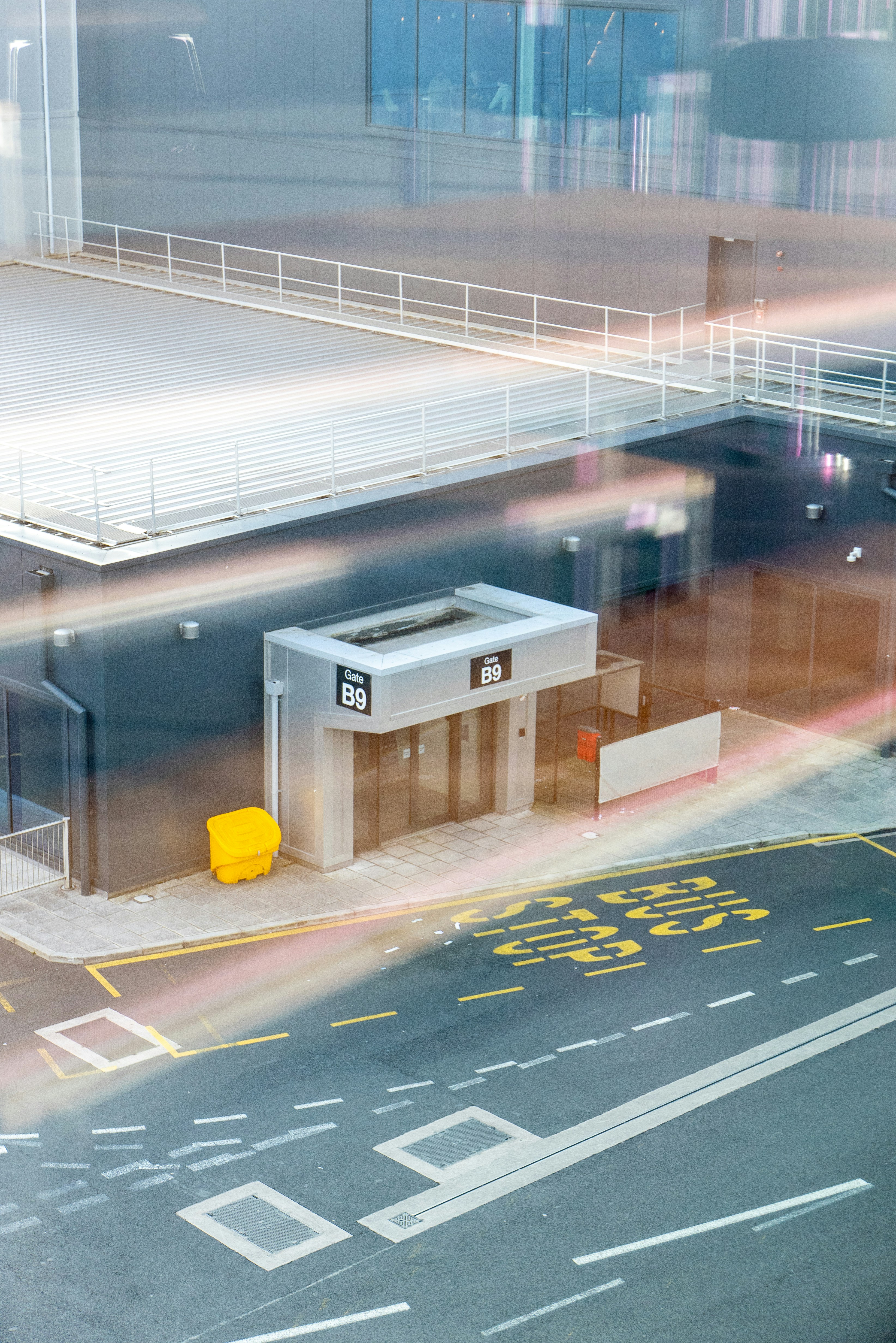 Overhead view of a modern glass-fronted building entrance labeled B9, with streaks of moving light crossing a street below.