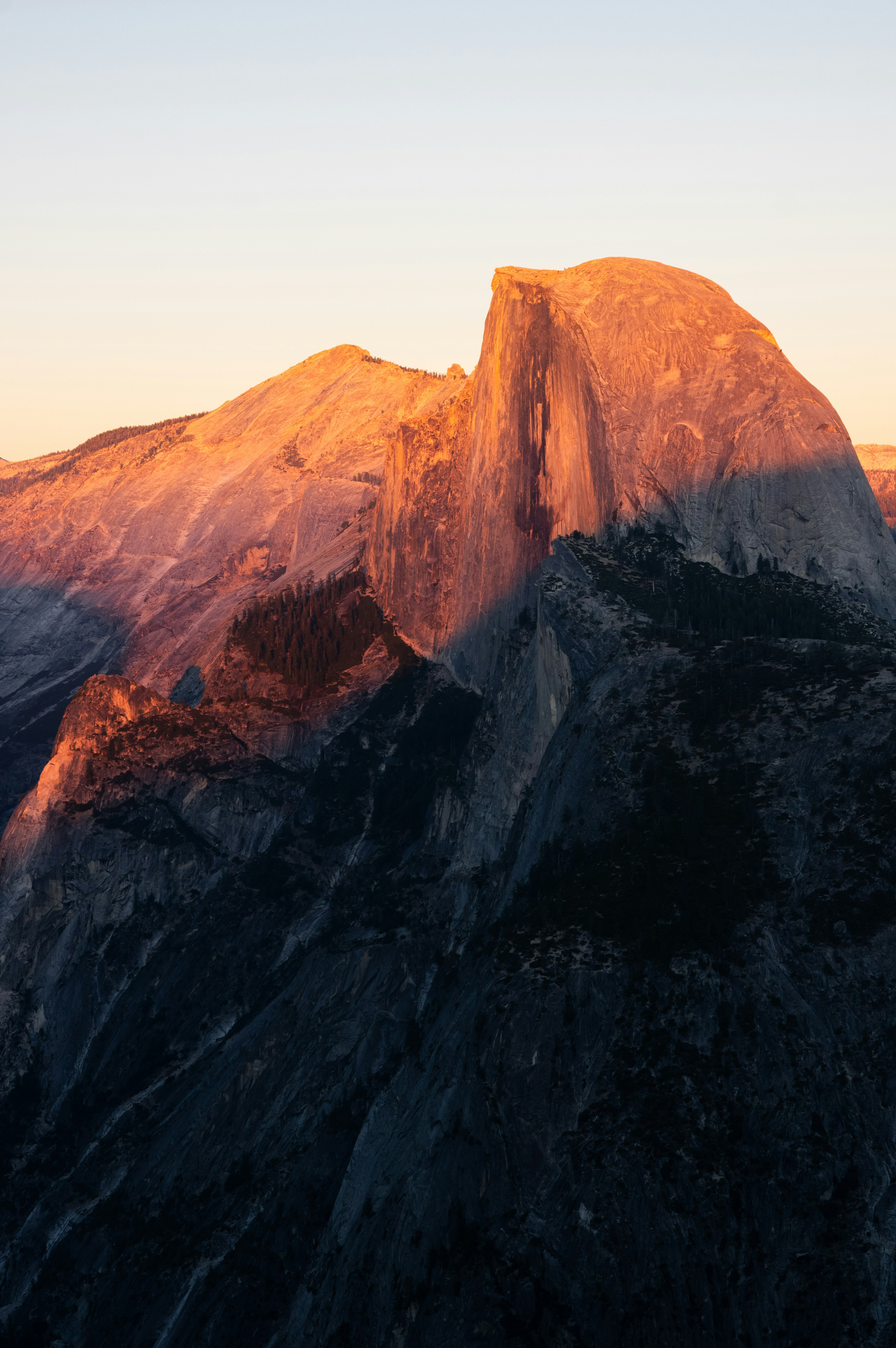 Granite peak bathed in warm sunset light, casting long shadows over jagged ridges. The photograph emphasizes the peak's texture and the contrast between sunlit facade and shadowed valley.