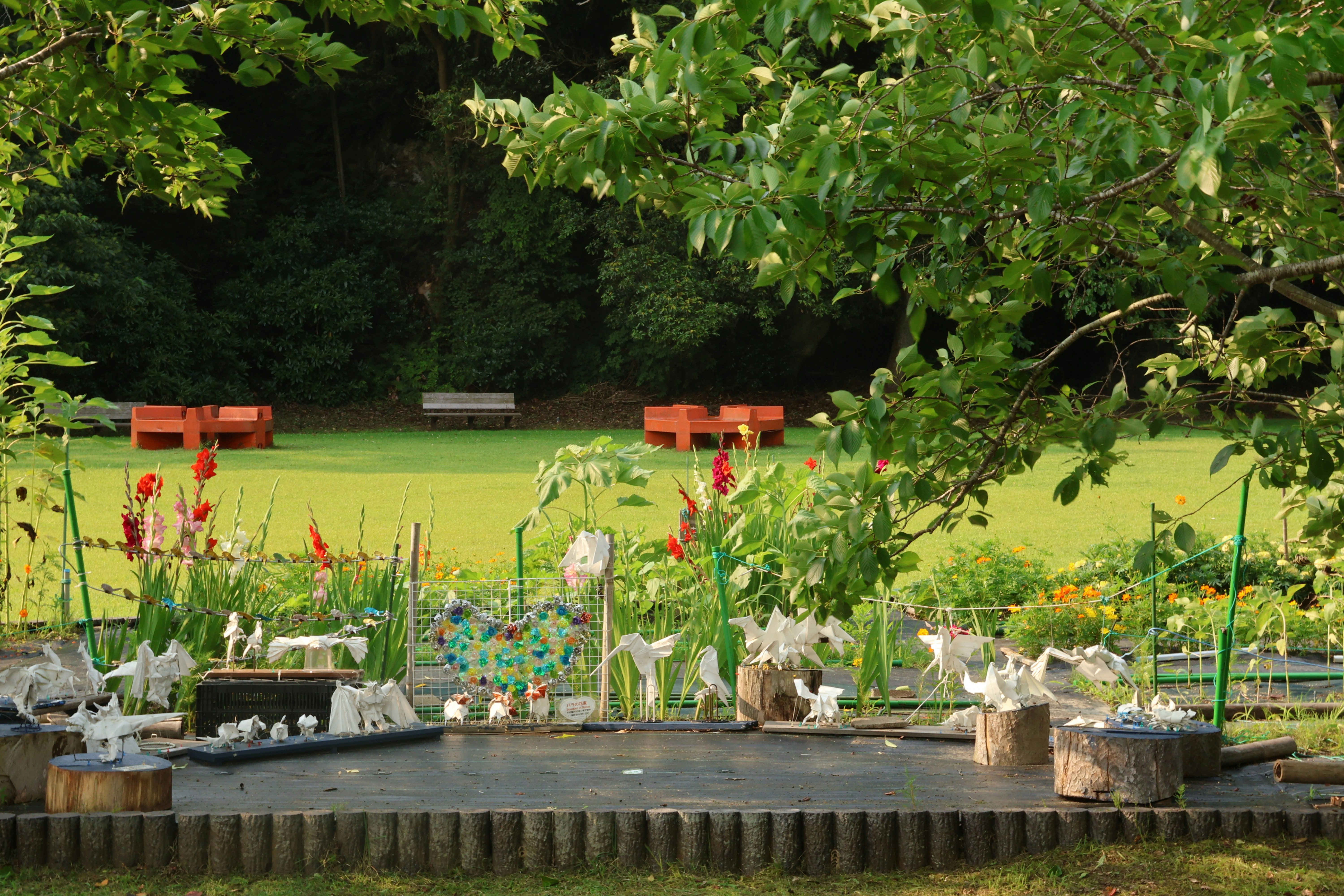 A tranquil garden scene featuring colorful flowers, sculptures, and benches amidst lush greenery. The arrangement invites reflection and connection with nature.
