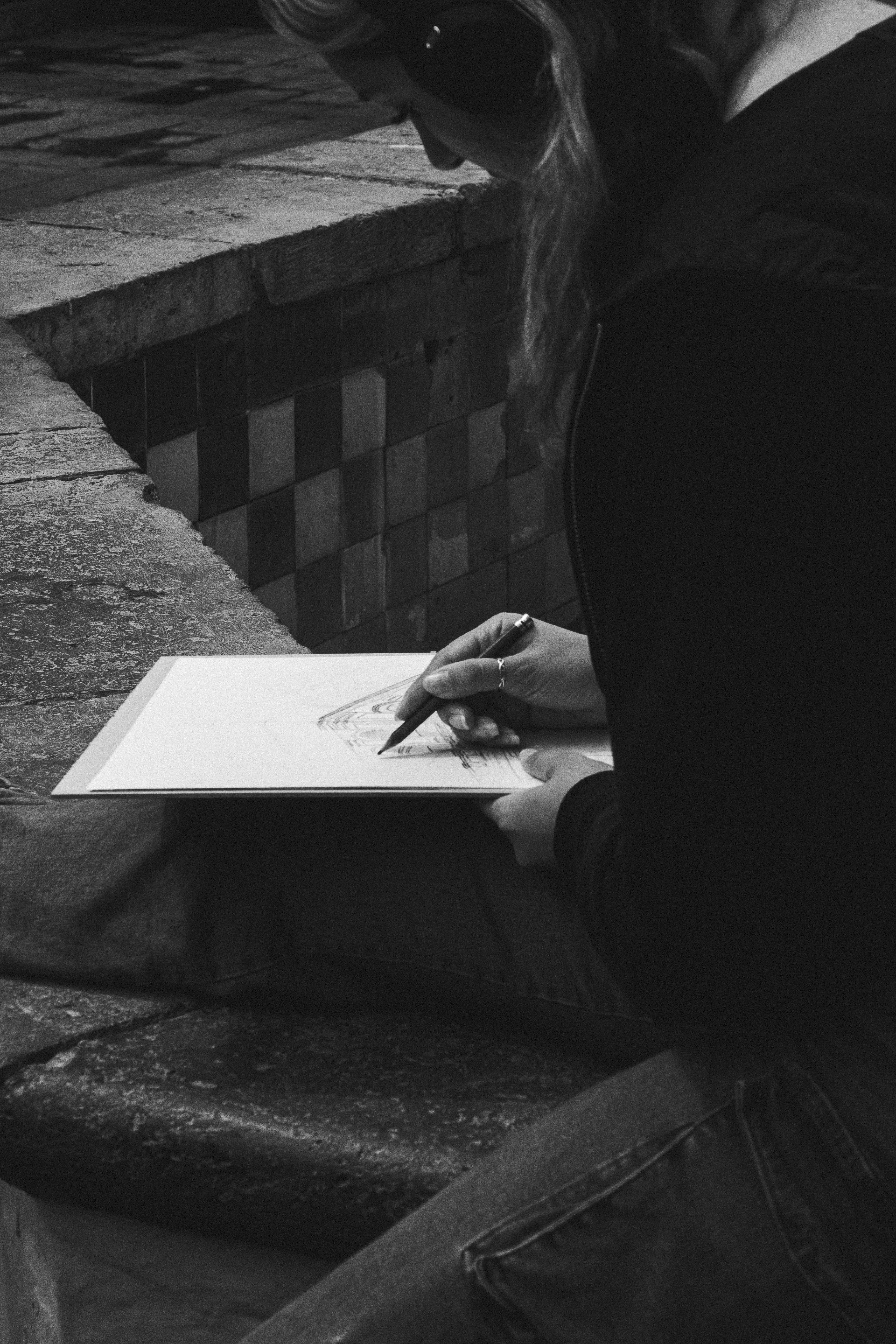 A woman sitting on a ledge writing on a piece of paper photo – Free ...