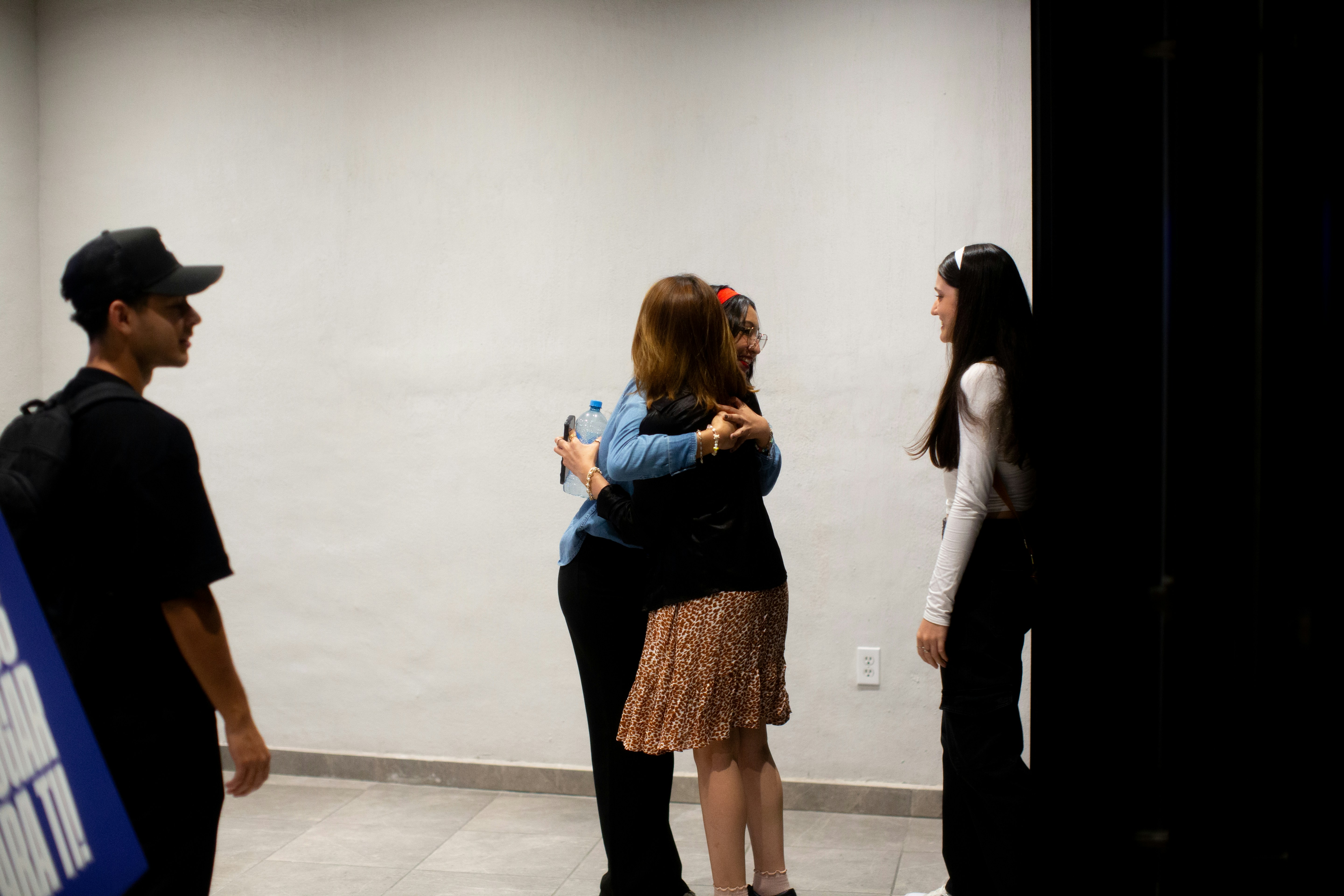 Two friends embracing warmly in a casual setting, surrounded by others engaging in conversation.