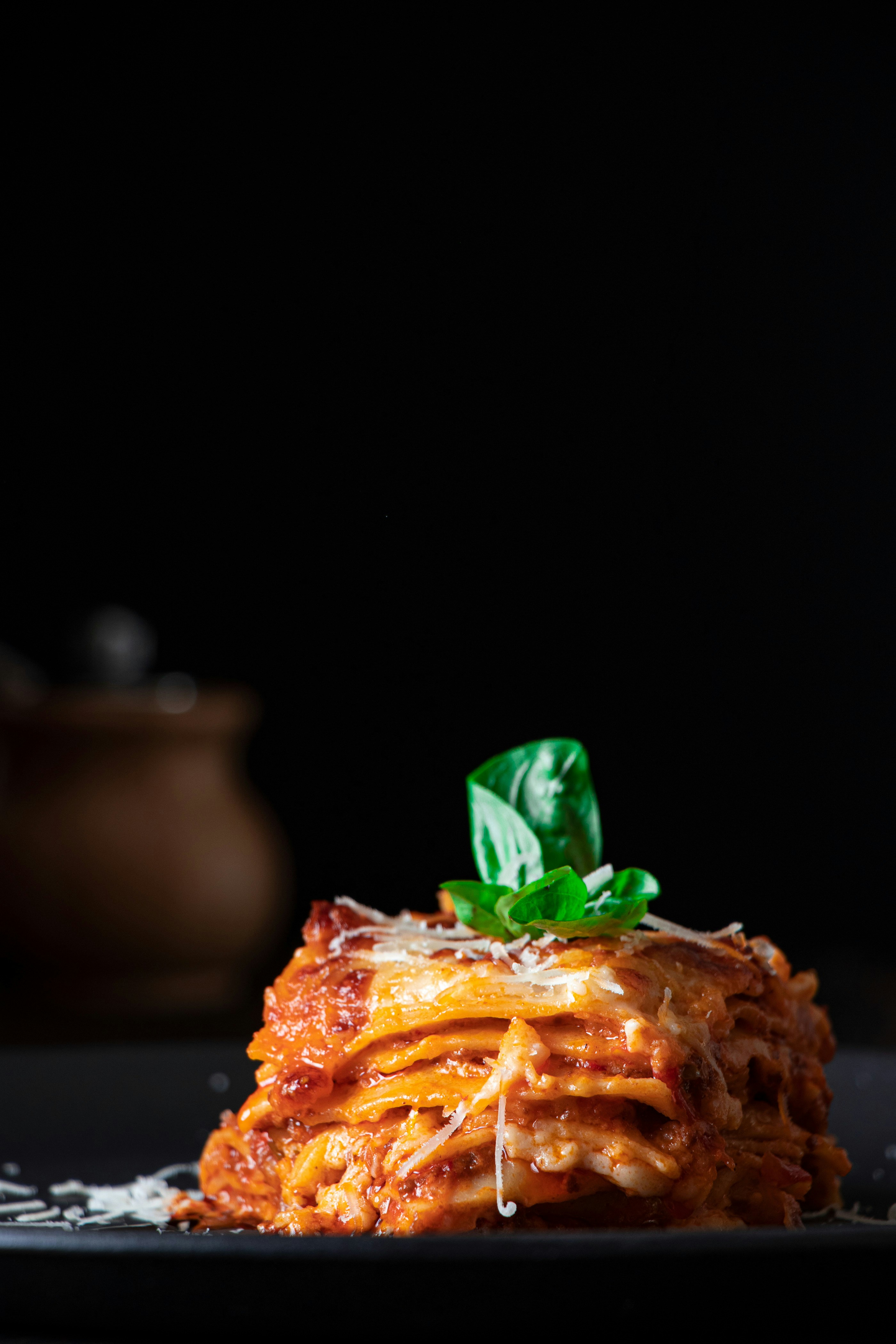 A black plate topped with lasagna covered in sauce and cheese photo ...